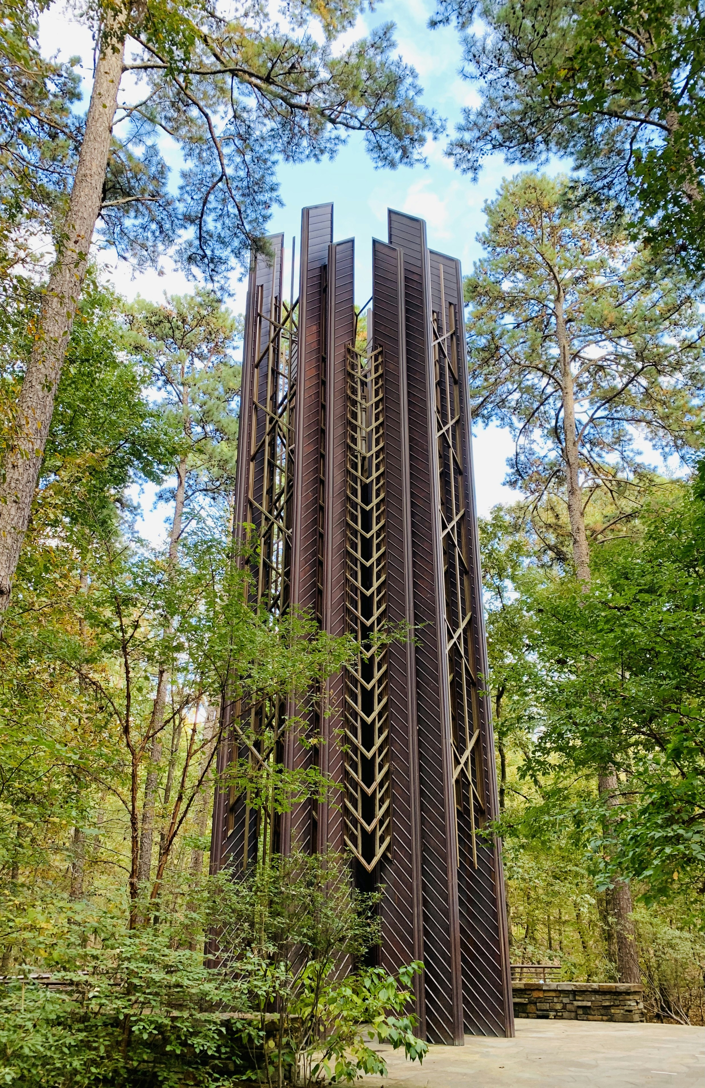 A striking modern structure rises amidst lush greenery, showcasing a unique design that contrasts with the surrounding forest. The tower's intricate patterns draw the eye upward.