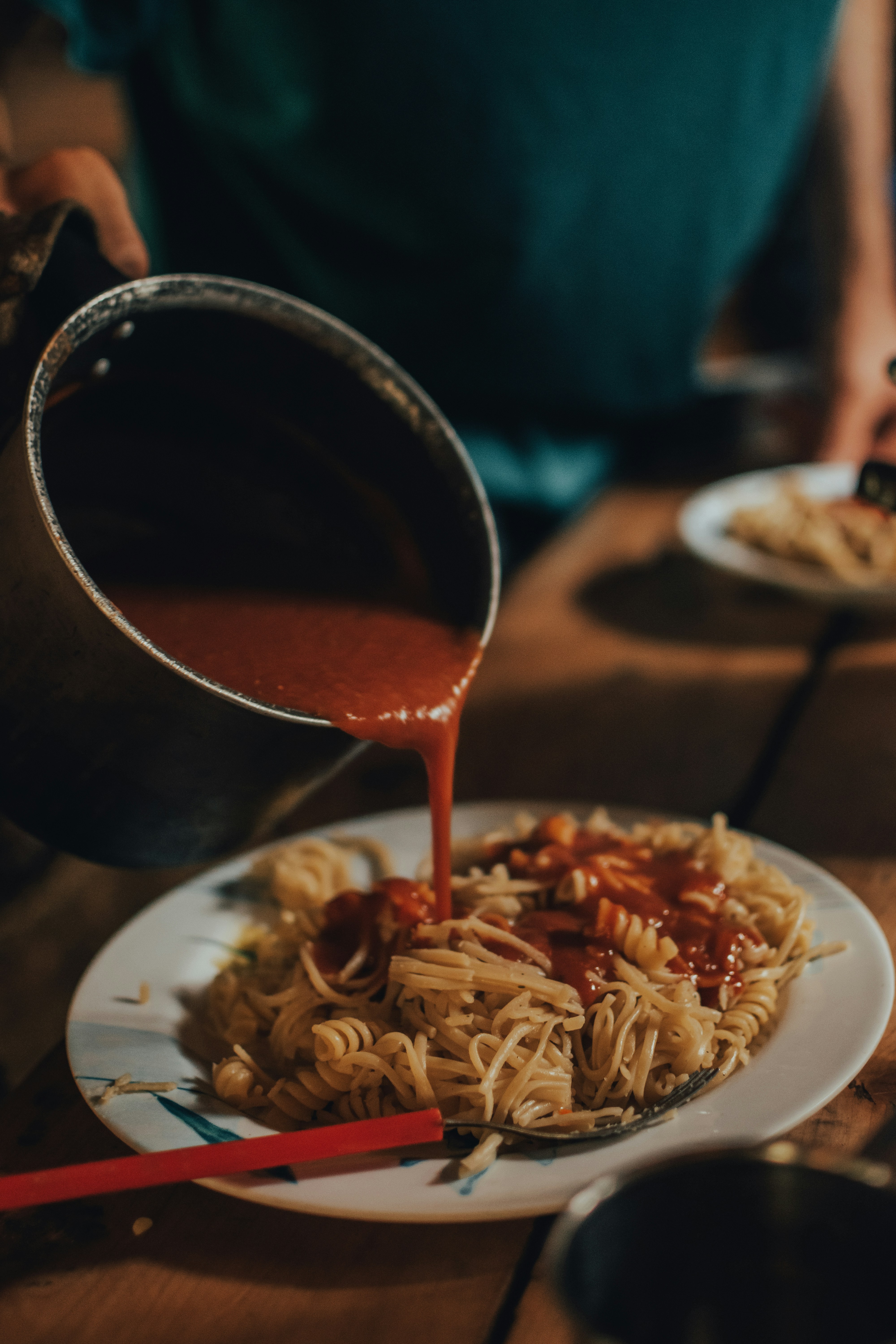 a person pouring sauce on a plate of noodles