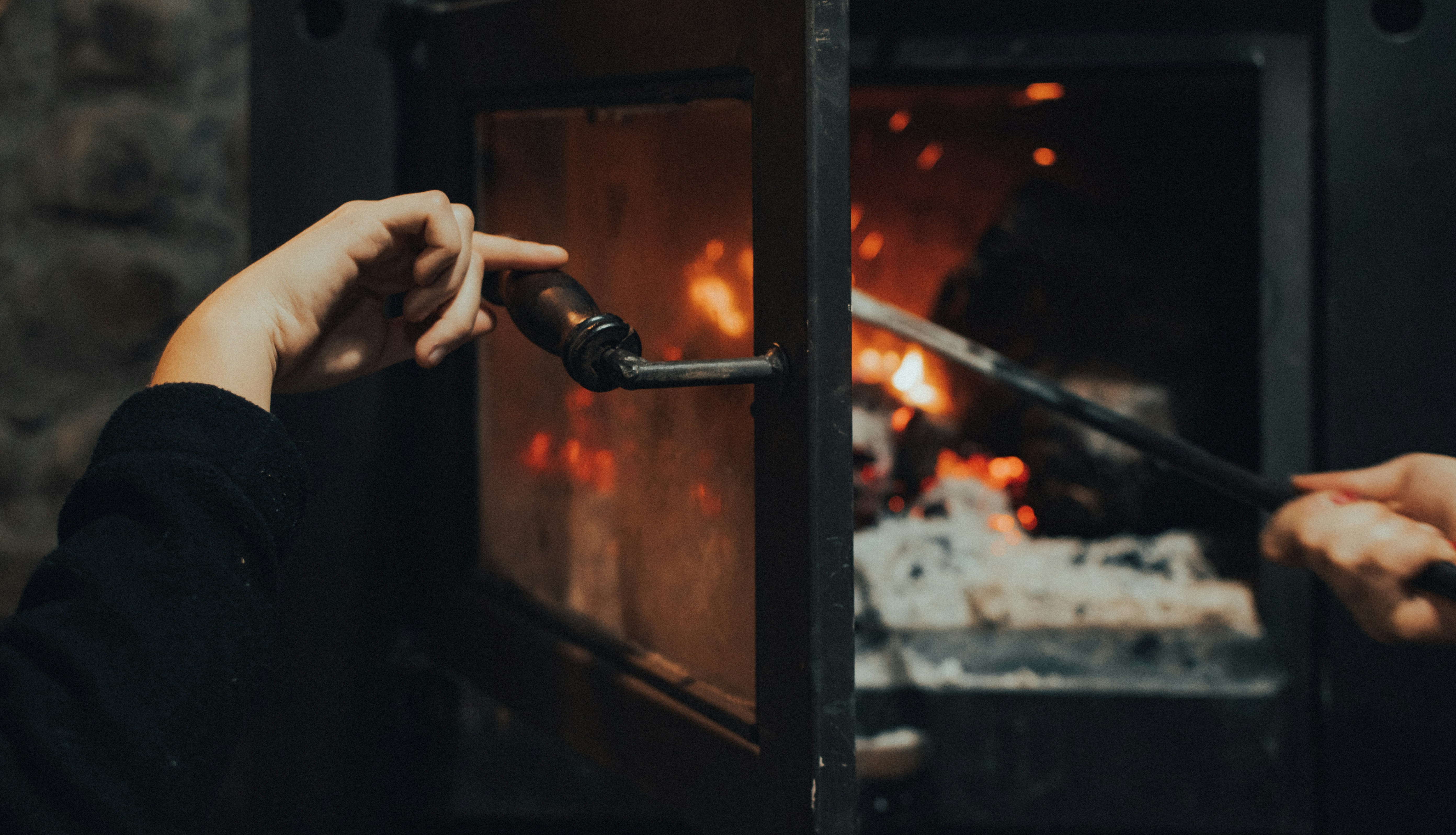 Doorway to Warmth: Two Hands Open the Wood Stove as Embers Glow