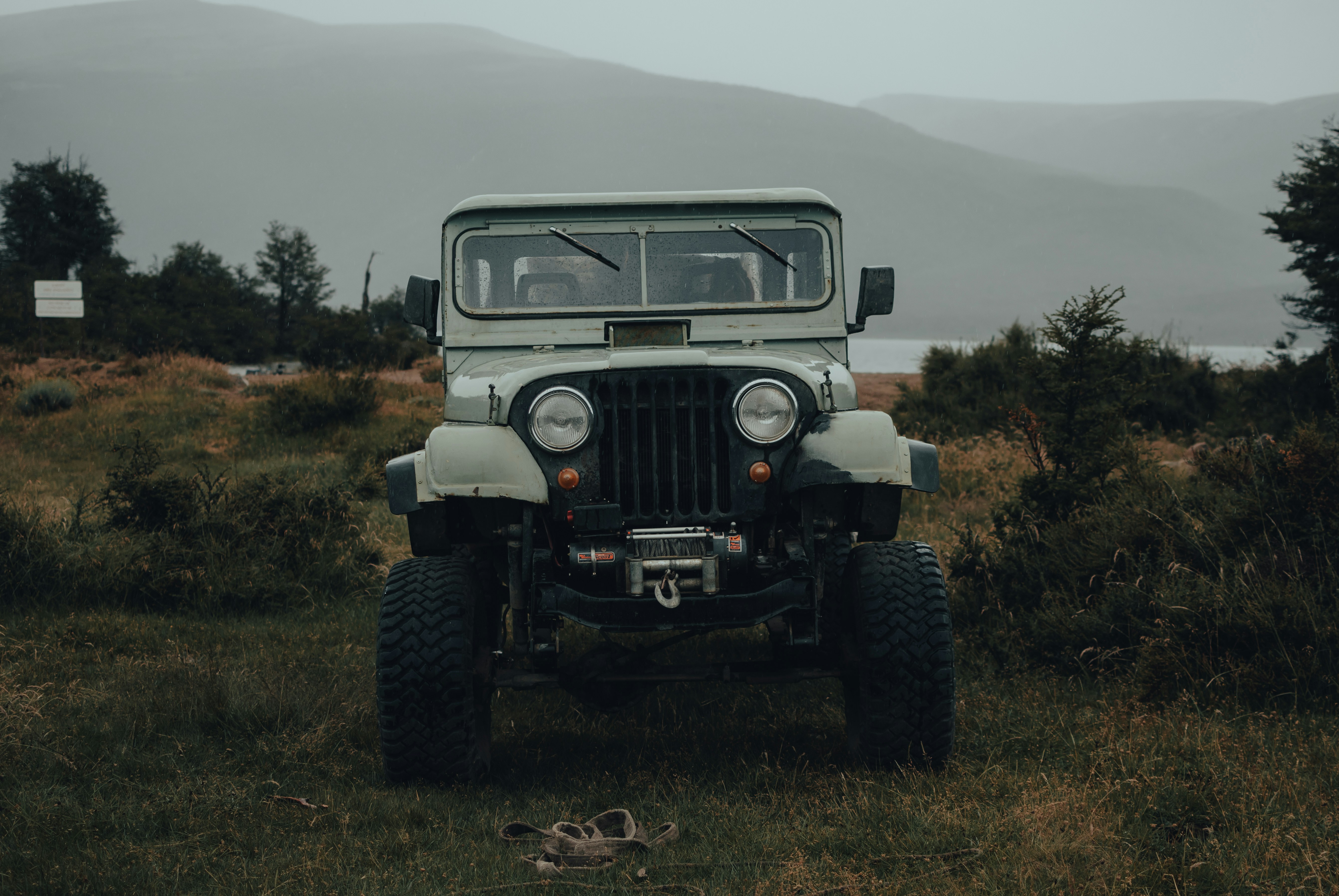 A classic off-road vehicle parked on a grassy field, surrounded by a moody landscape of rolling hills and distant trees.