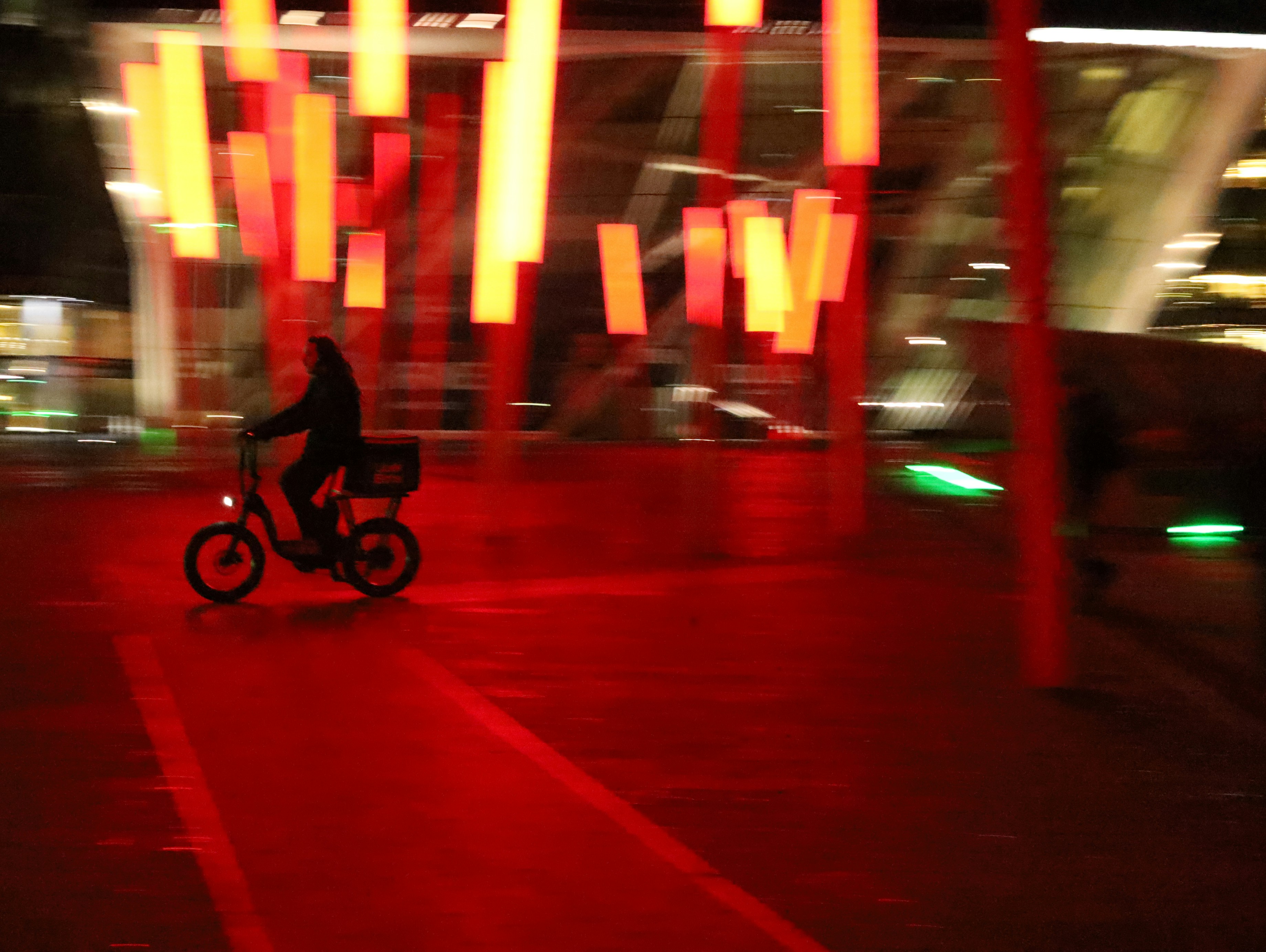 Cyclist in motion at night with vibrant red lights reflecting in an urban setting.