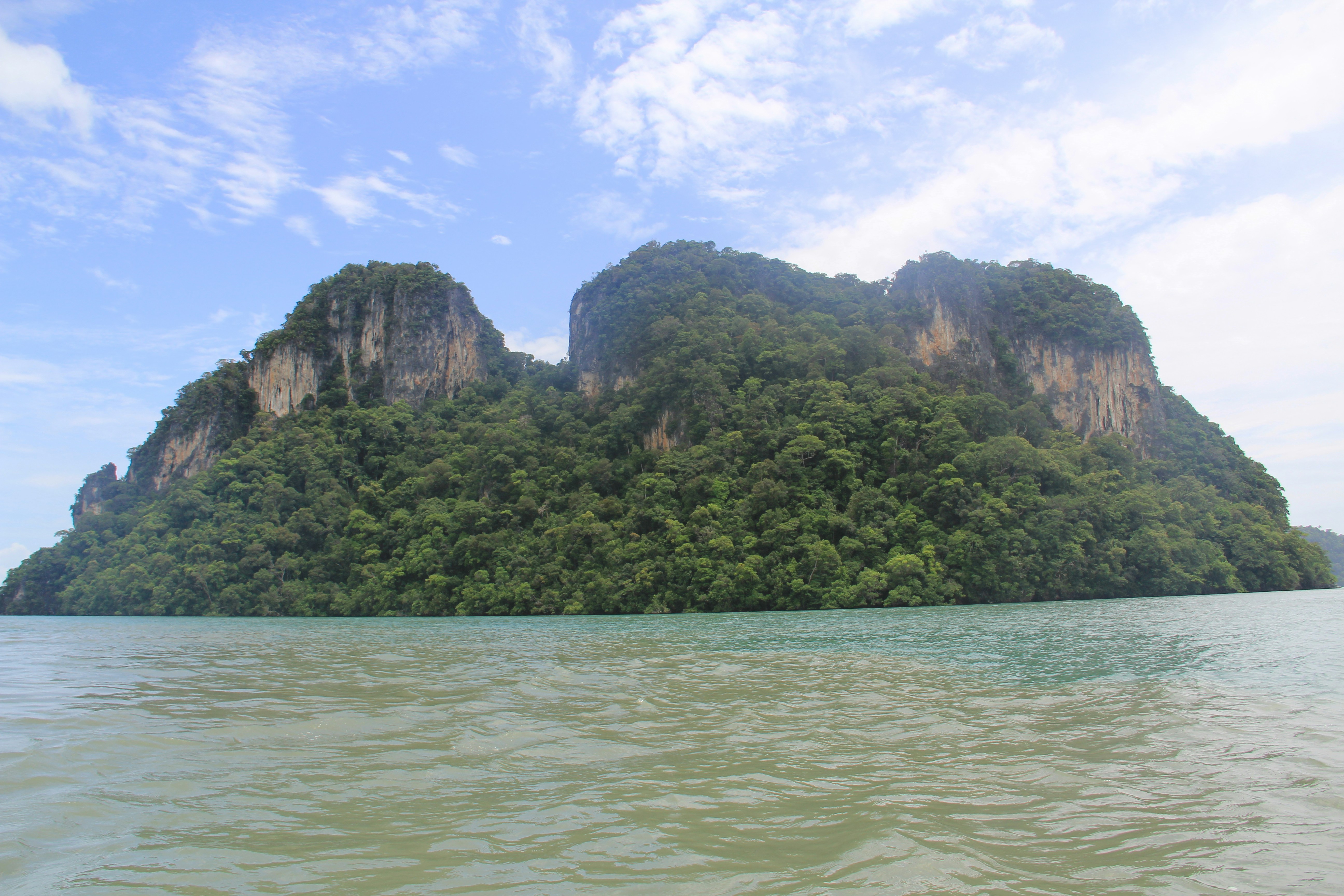 Lush green island with steep cliffs rising from tranquil waters under a partly cloudy sky.