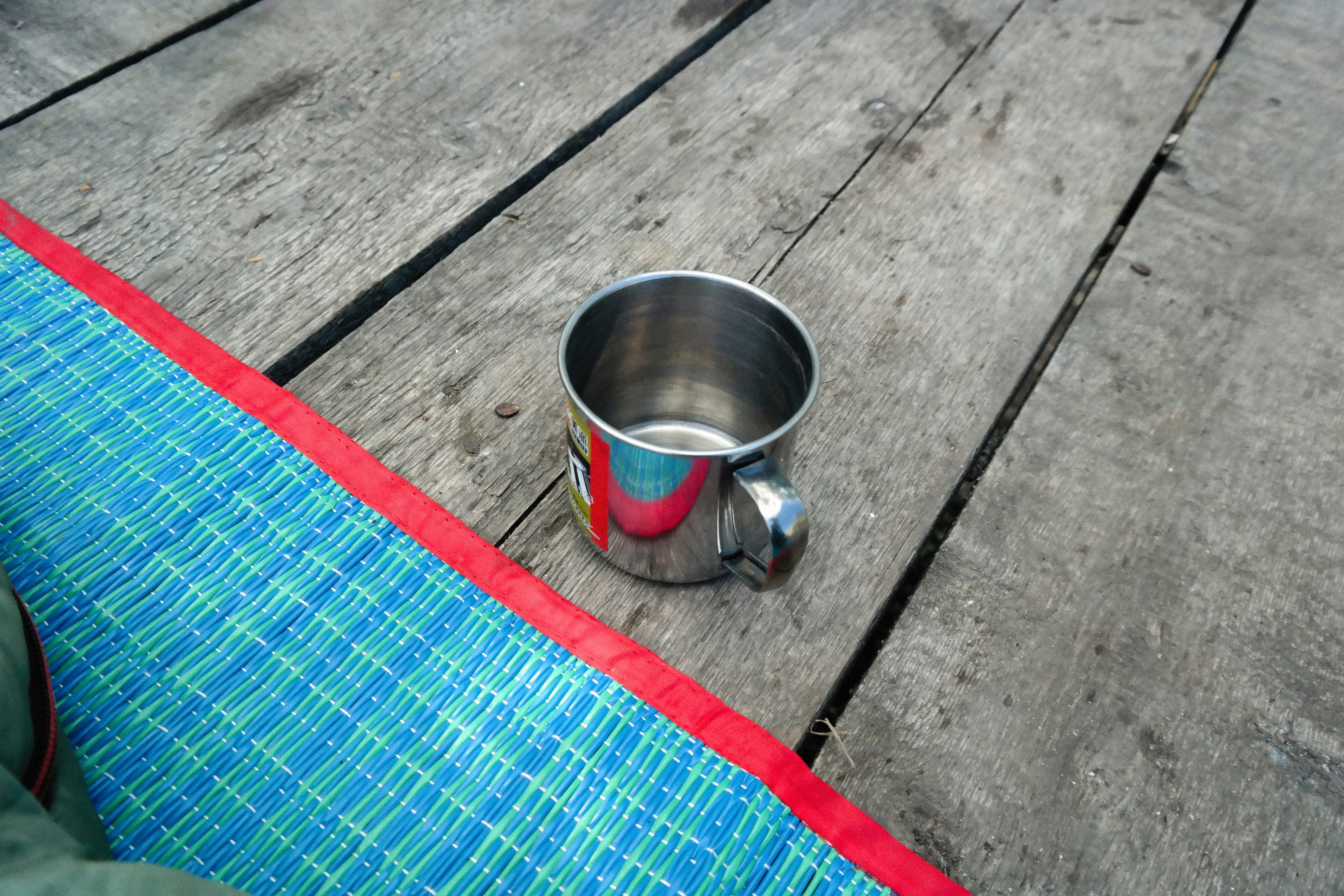 Stainless Cup on a Weathered Deck Next to a Colorful Mat