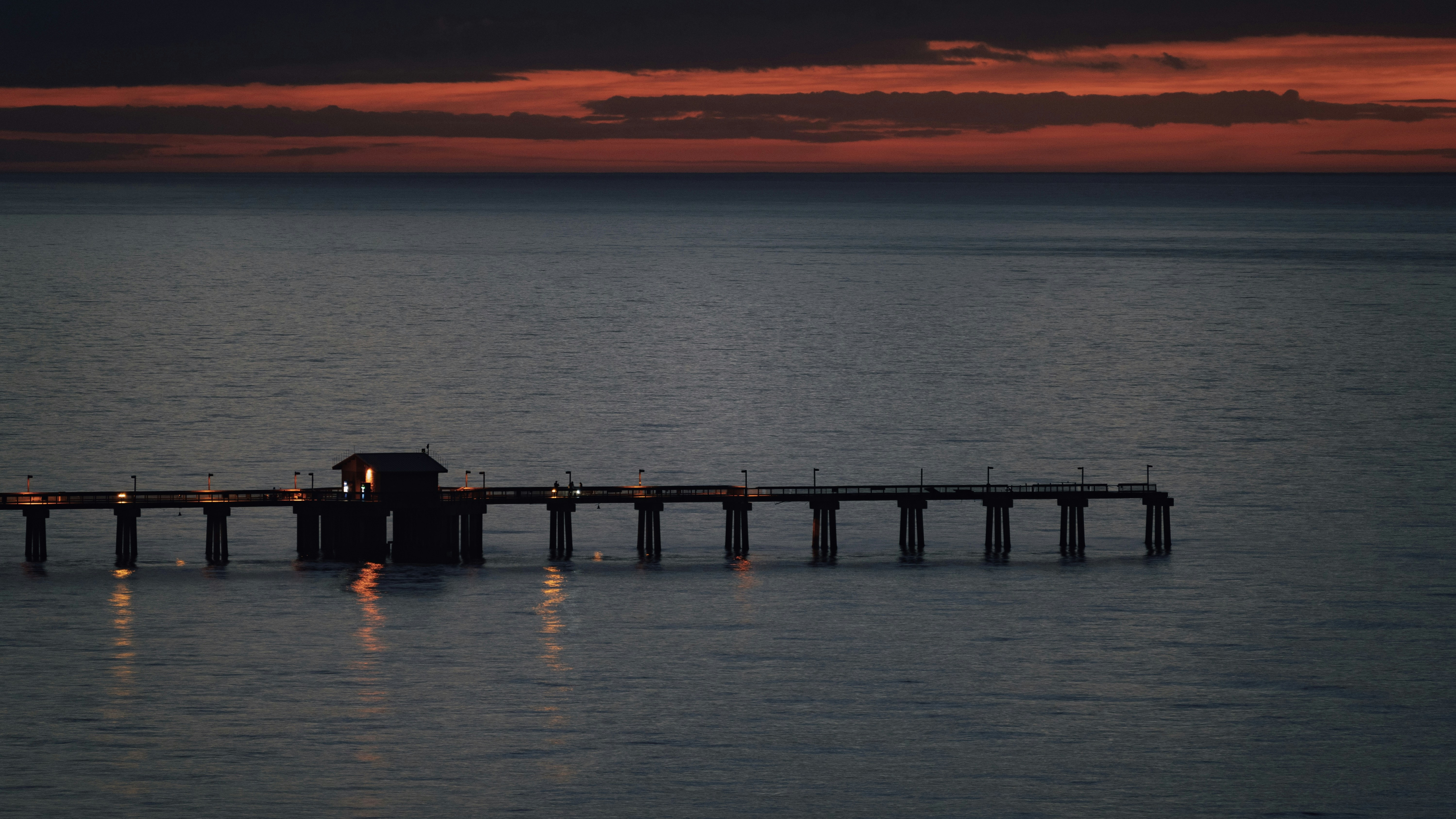 A serene pier extending into calm waters, illuminated by soft lights against a backdrop of a colorful twilight sky.