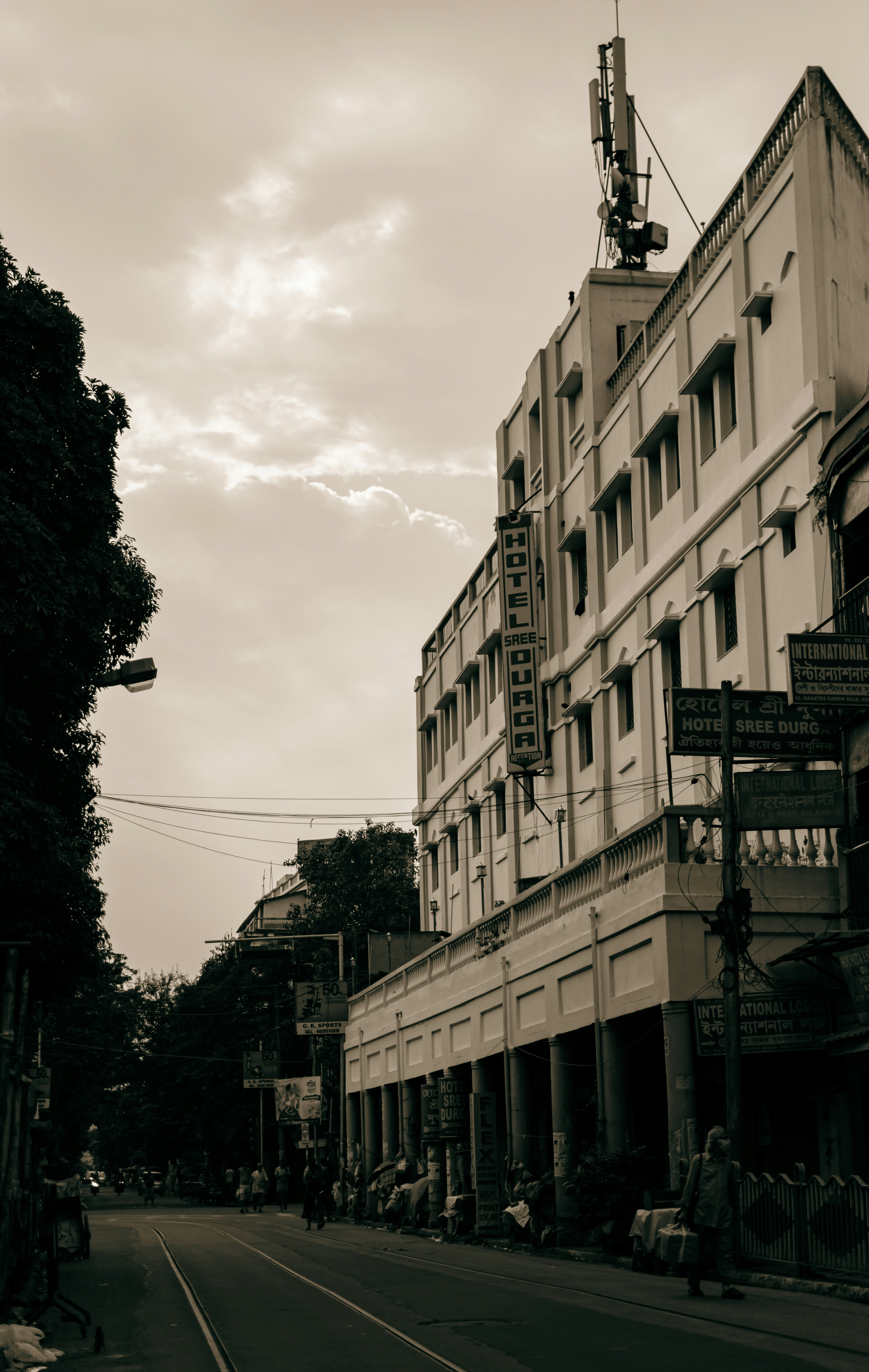 Historic hotel building with vintage signage lining a quiet urban street, framed by lush trees and an overcast sky.