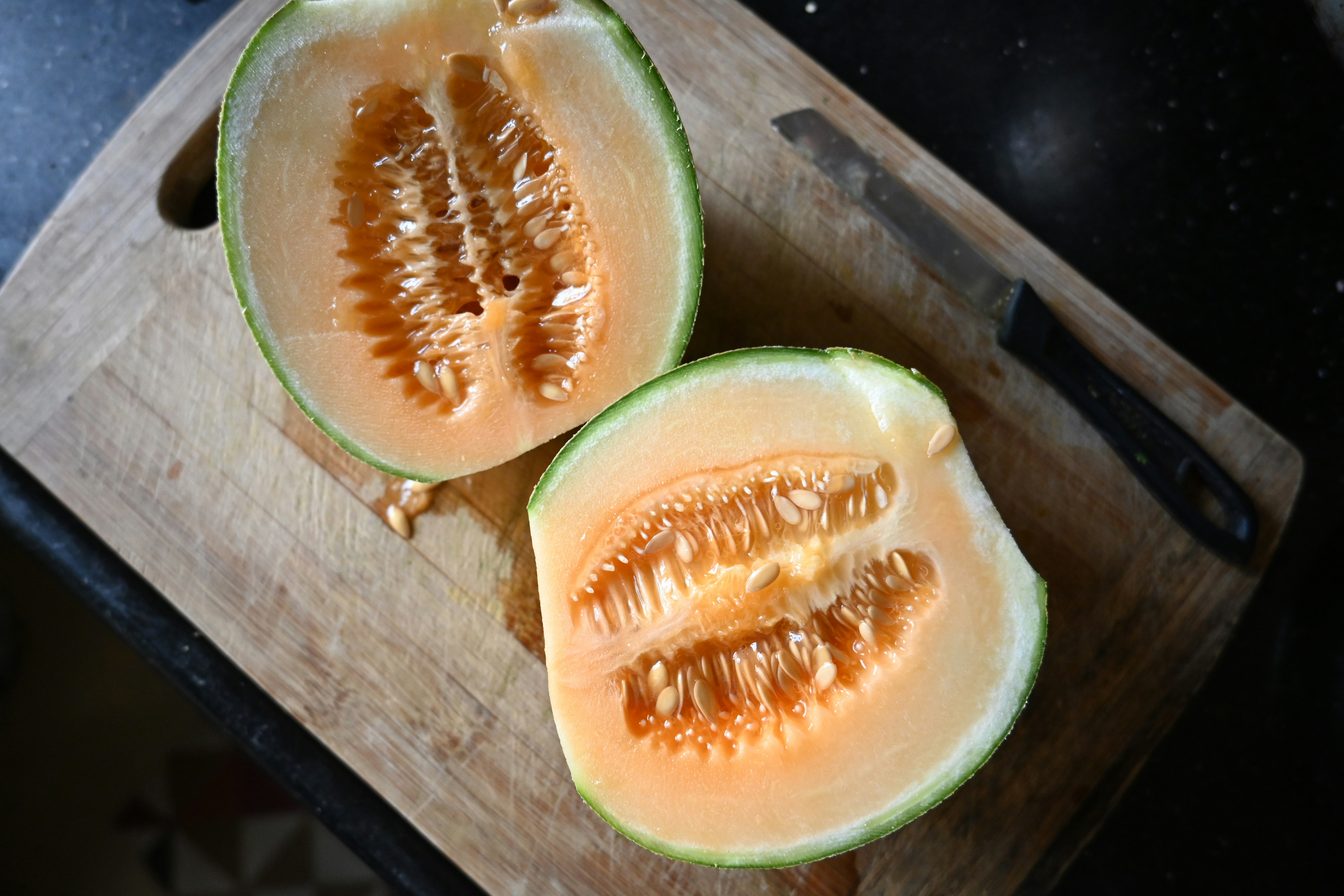 Freshly cut melon halves revealing vibrant orange flesh and seeds on a wooden cutting board.