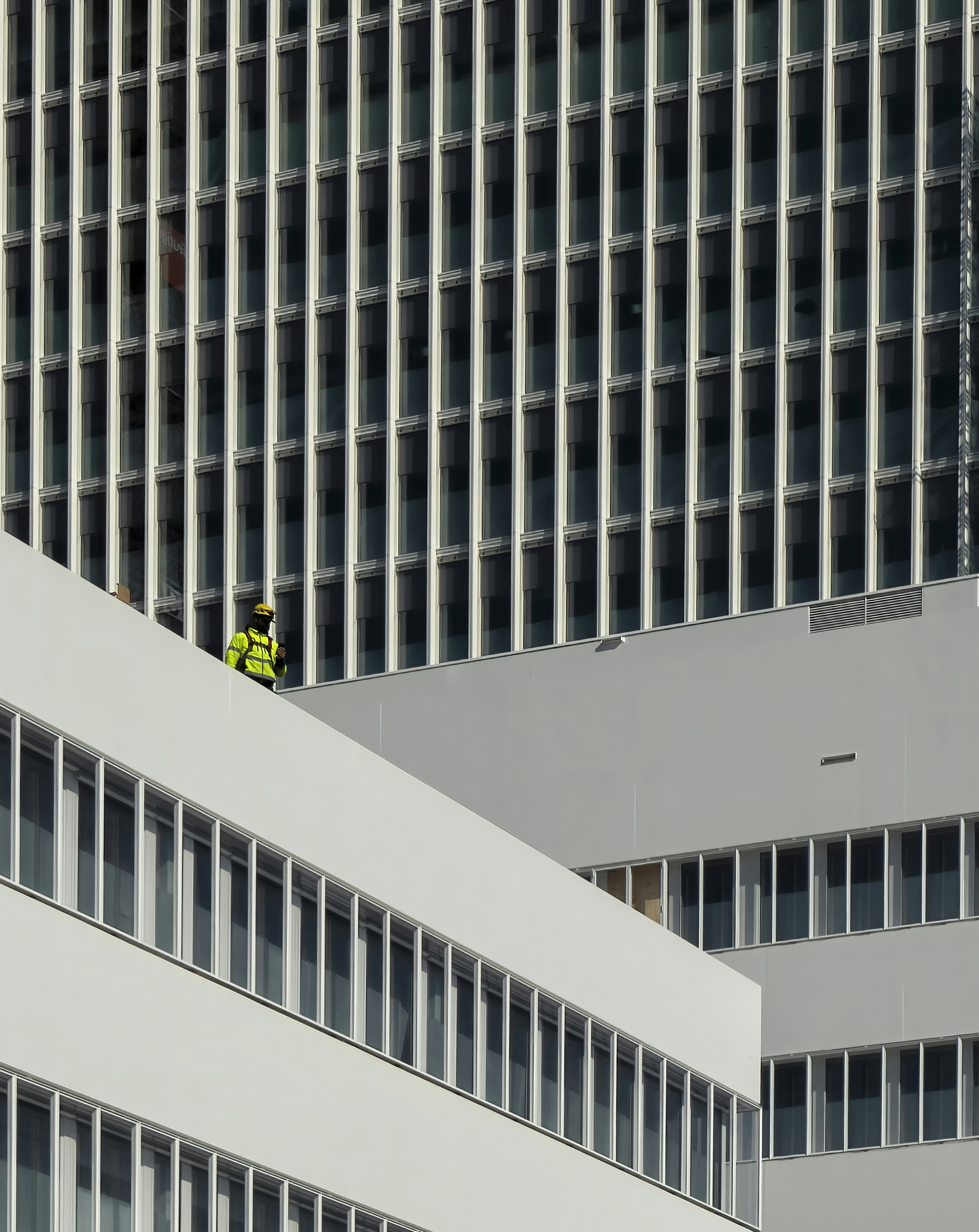 On the Edge of Glass: A Yellow-Vested Figure on a Diagonal Rooftop