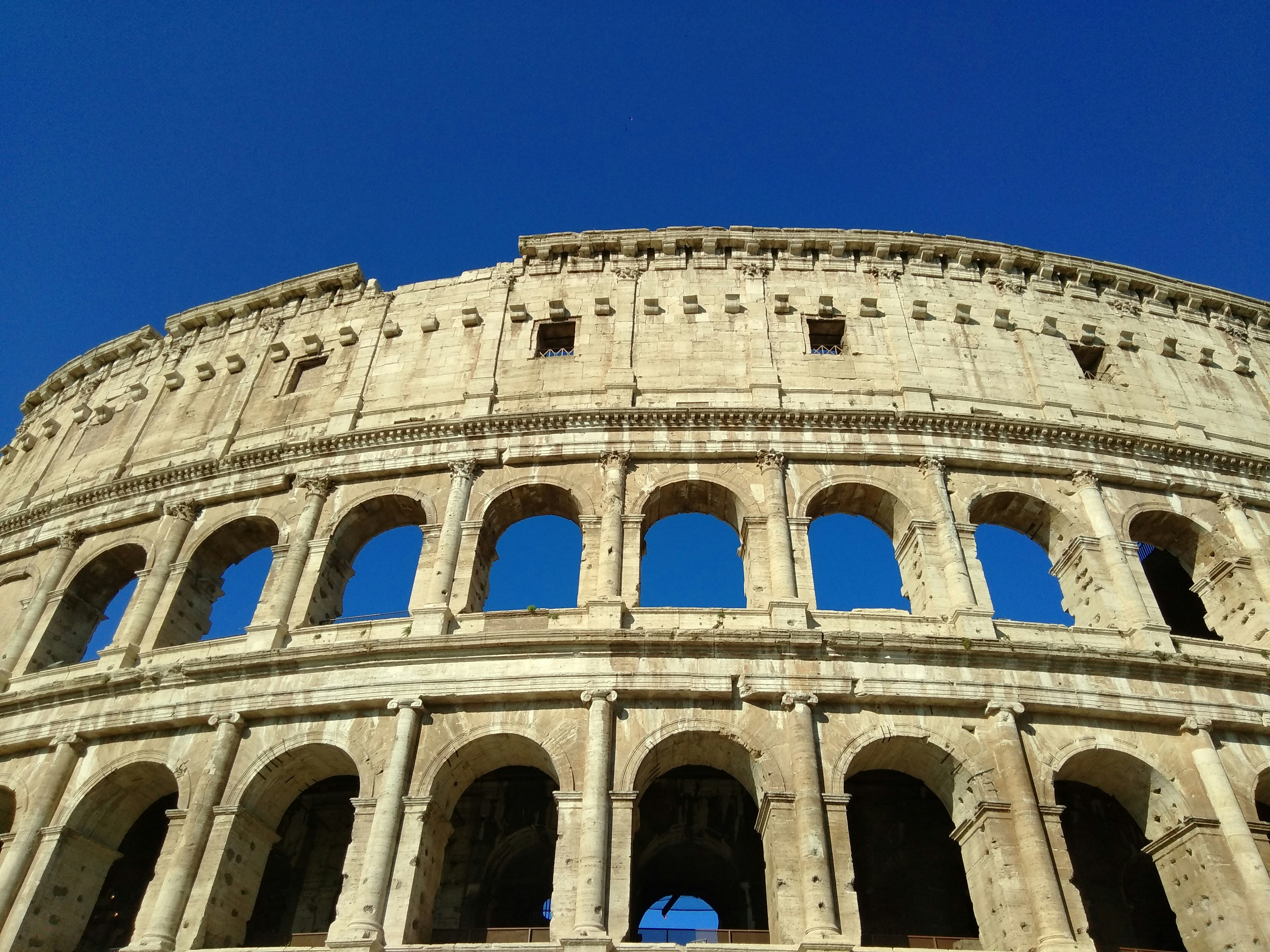 The majestic Colosseum stands tall against a clear blue sky, showcasing its intricate architecture and historical significance.