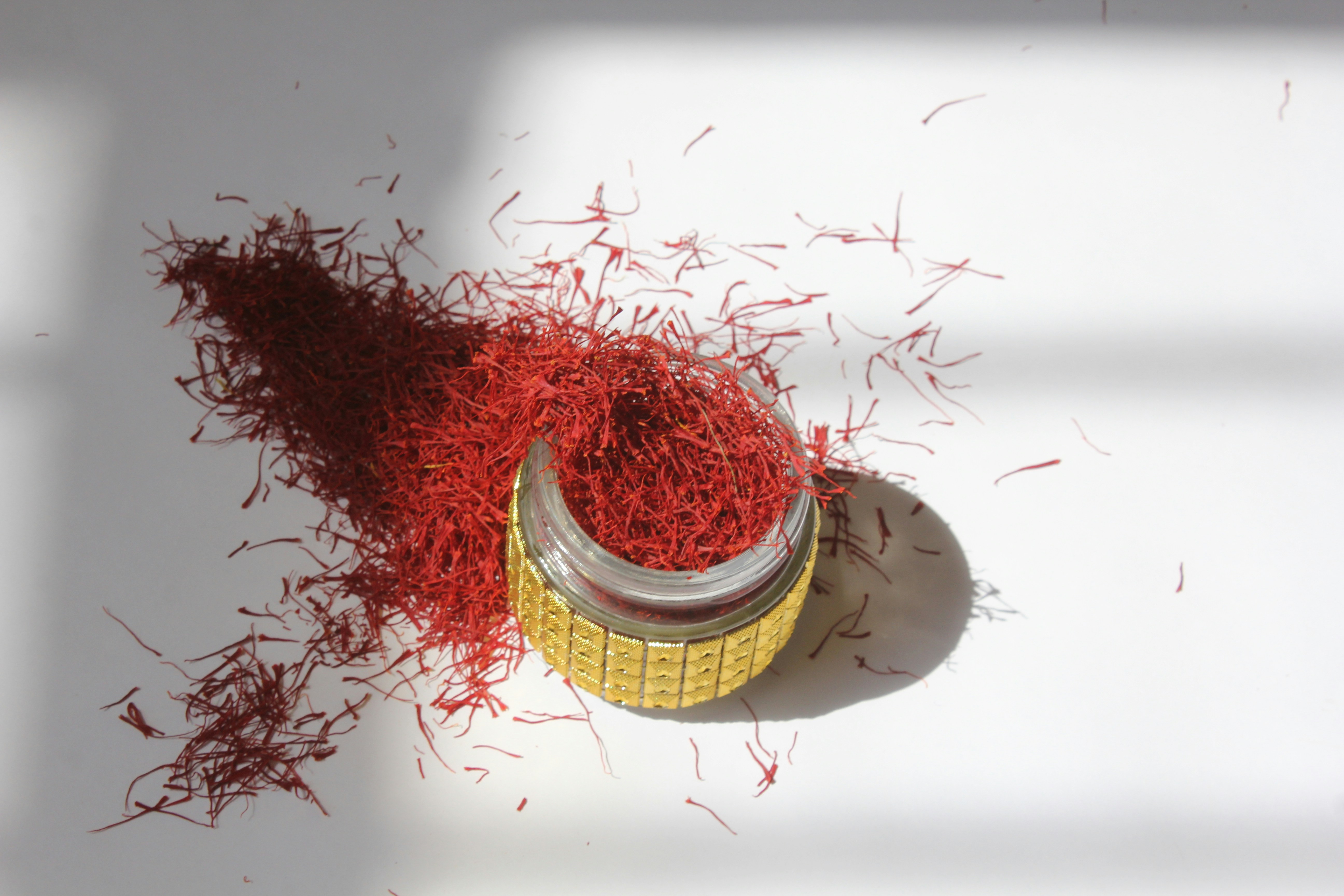 Glass jar of vibrant saffron threads casting shadows on a white surface.