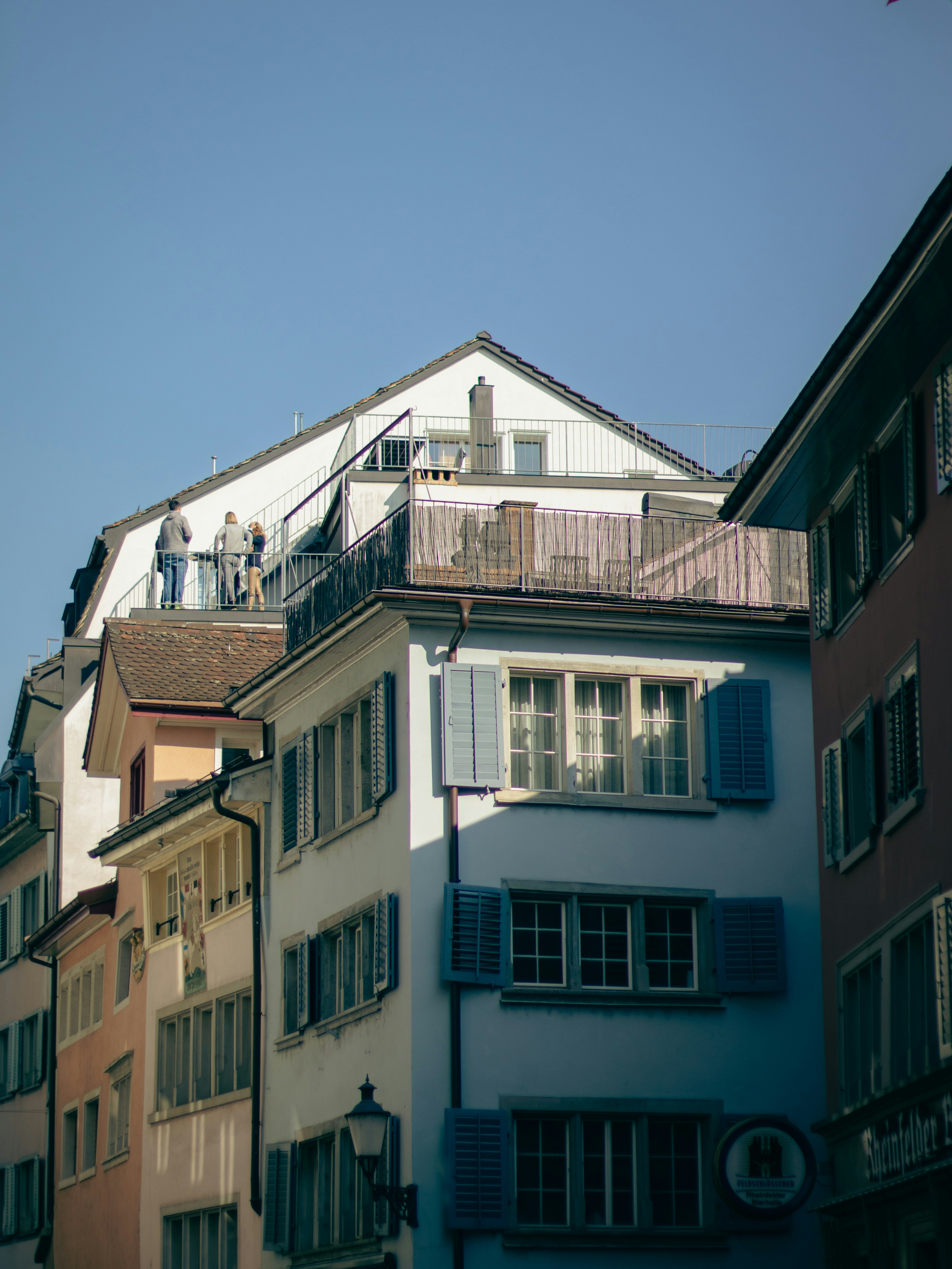 People enjoying a rooftop gathering atop a charming building in Zurich, showcasing the city's architectural beauty under a clear sky.