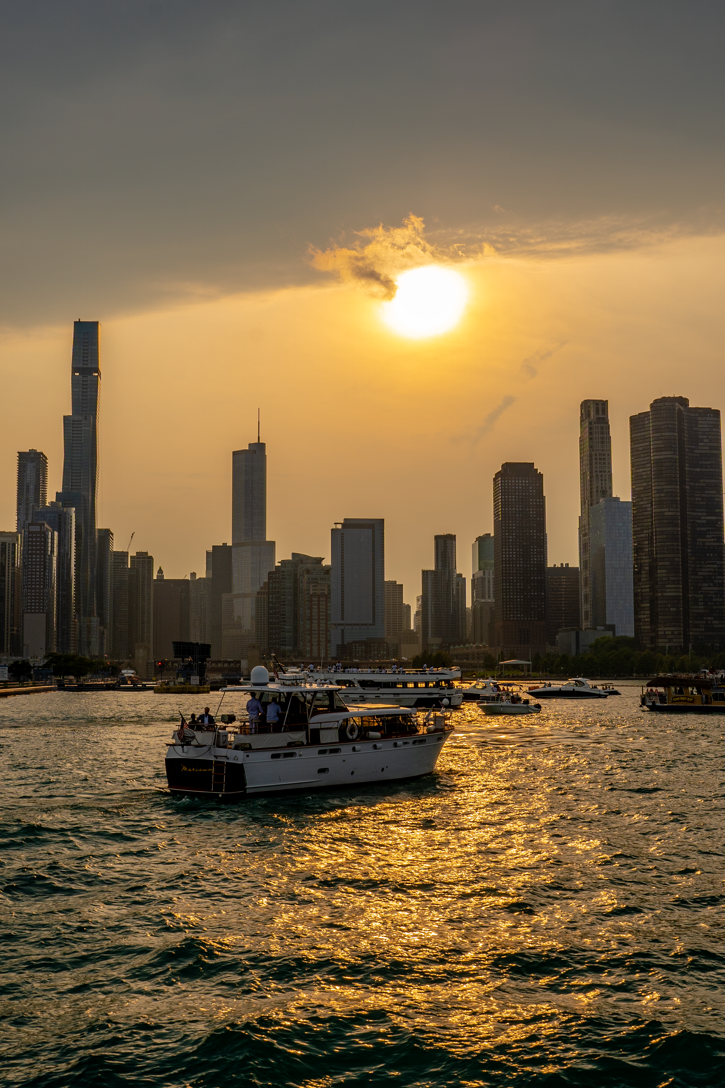 A luxurious boat glides through shimmering waters, framed by a skyline of towering skyscrapers under a golden sunset.