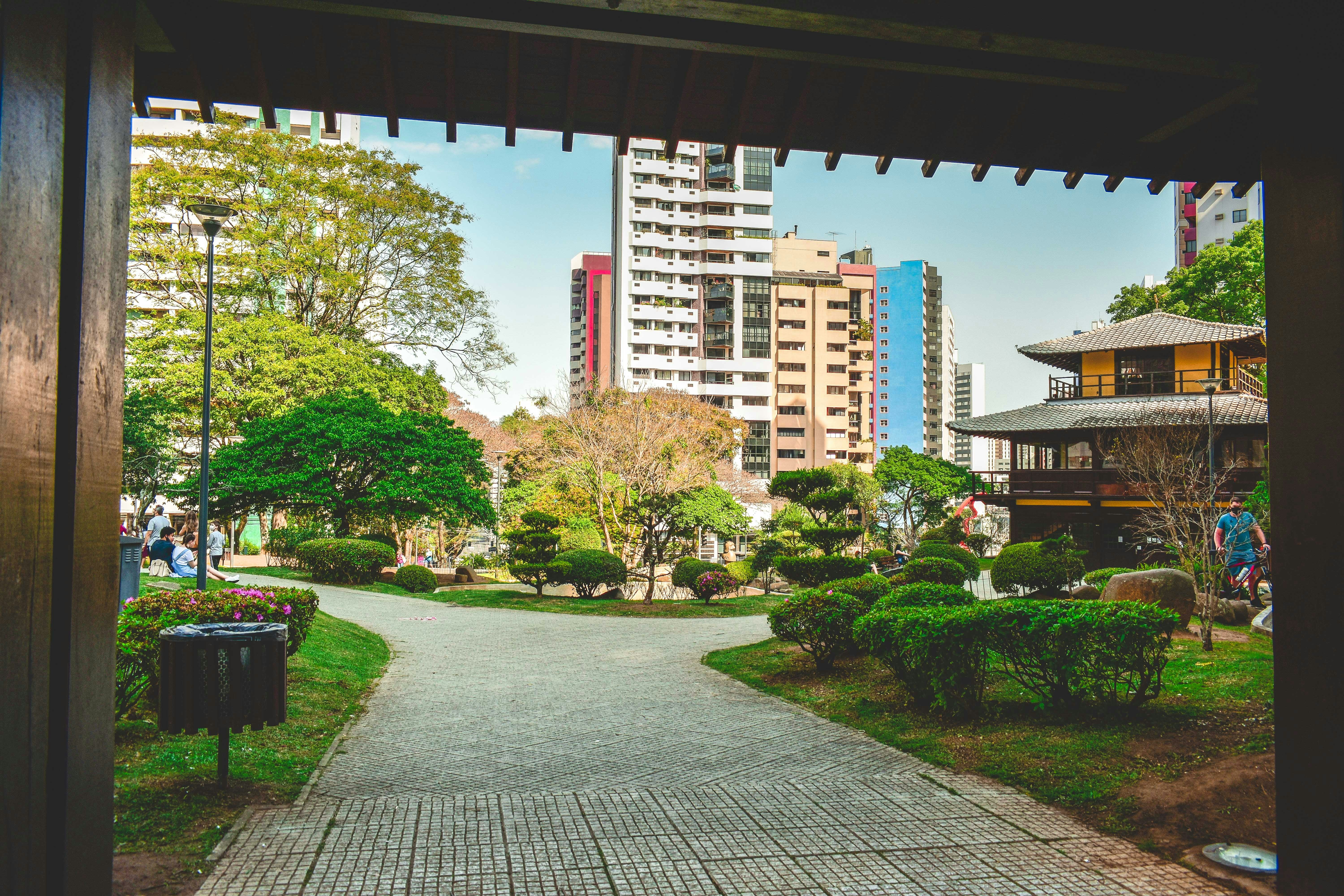 a view of a walkway through a park with tall buildings in the background