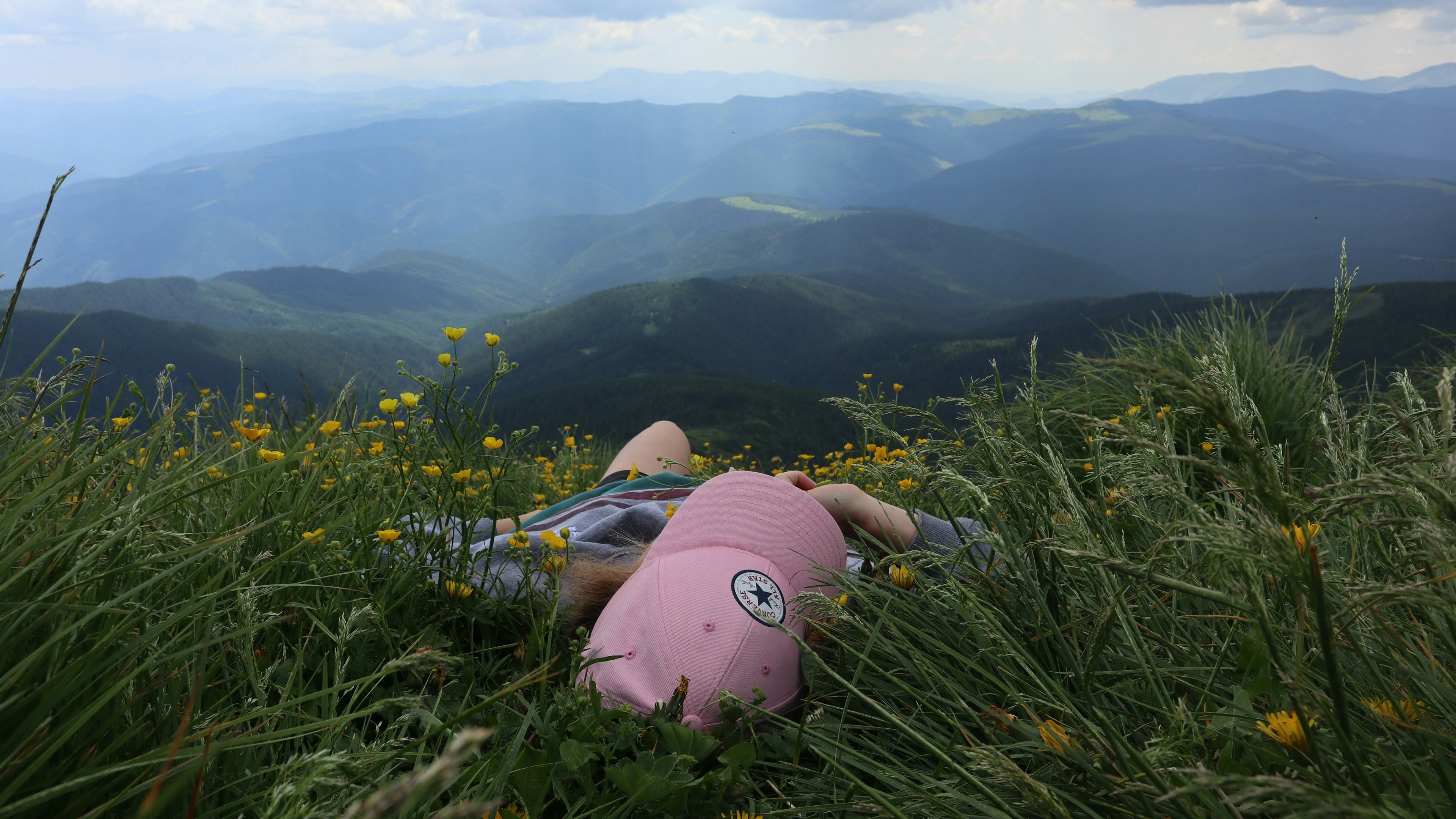 Pink helmeted climber resting among alpine wildflowers with distant blue ridges