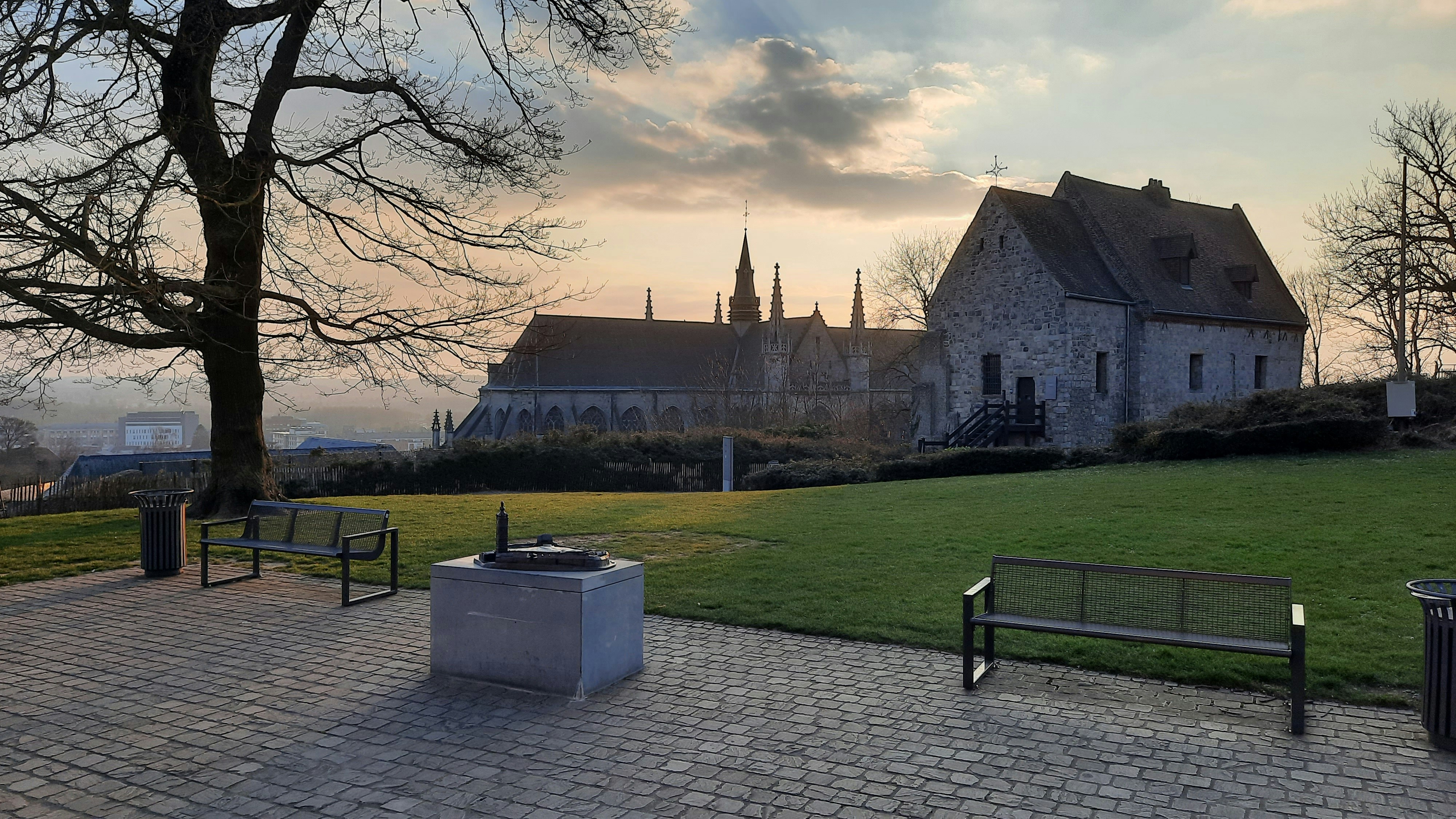 Historic building and spires under a pastel sky at dusk, with a foreground of benches and a stone walkway.