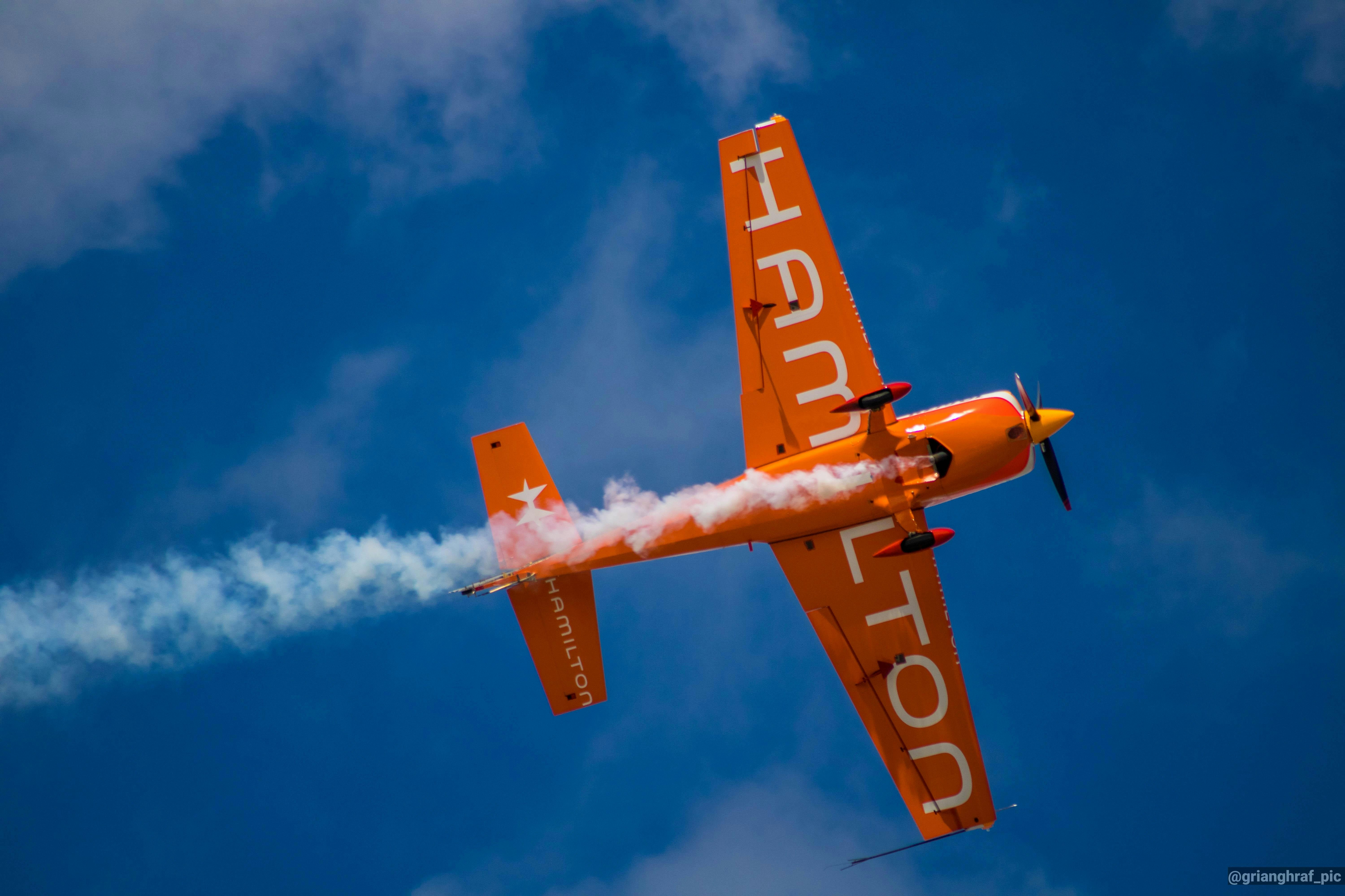 A small orange airplane flying through a blue sky photo – Free ...