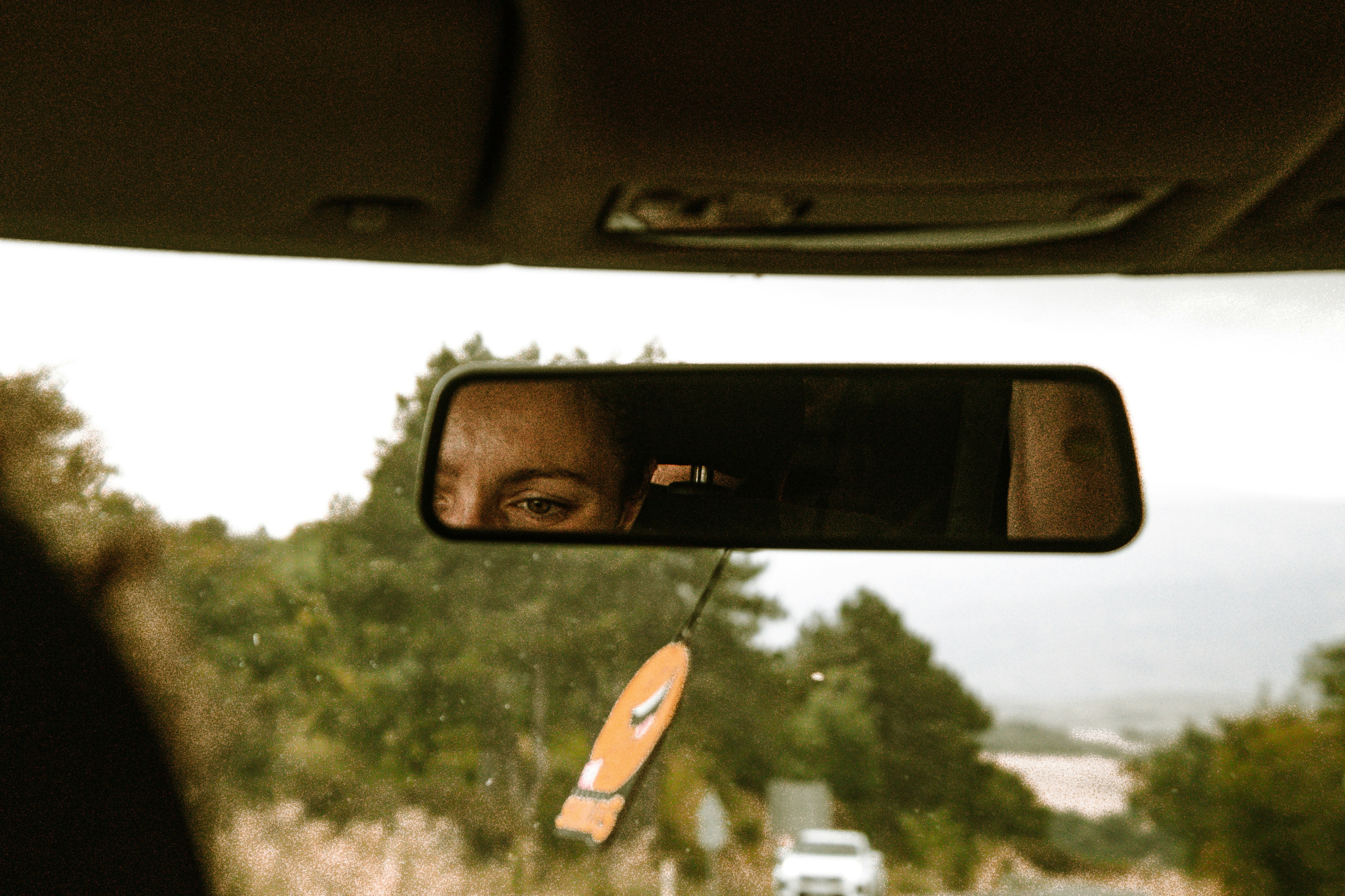 A close-up view of a driver's reflection in a rearview mirror, capturing a moment of contemplation amidst a scenic drive.