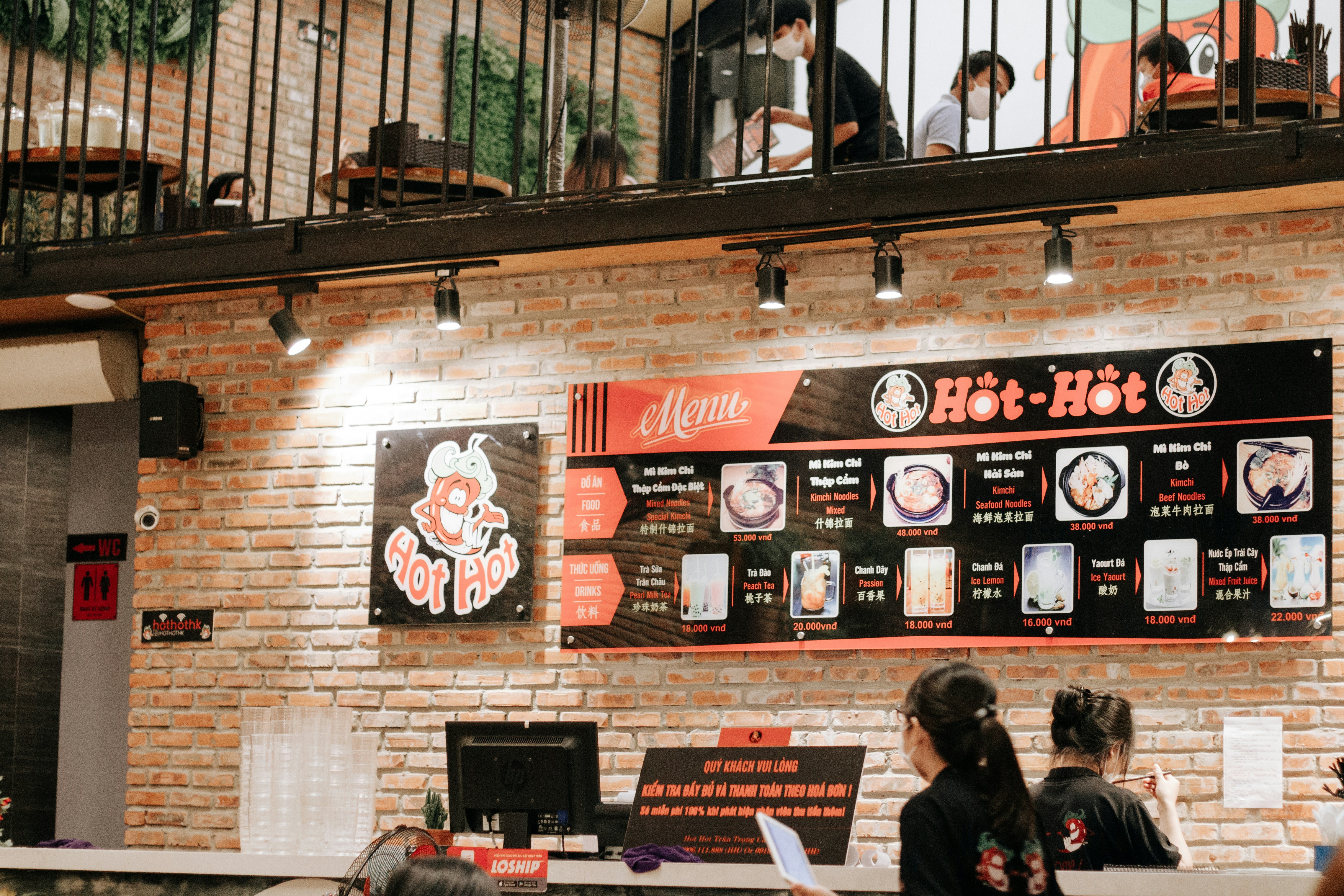 A vibrant restaurant interior featuring a menu board and a lively atmosphere with staff engaging with customers. The design blends contemporary elements with a cozy ambiance.