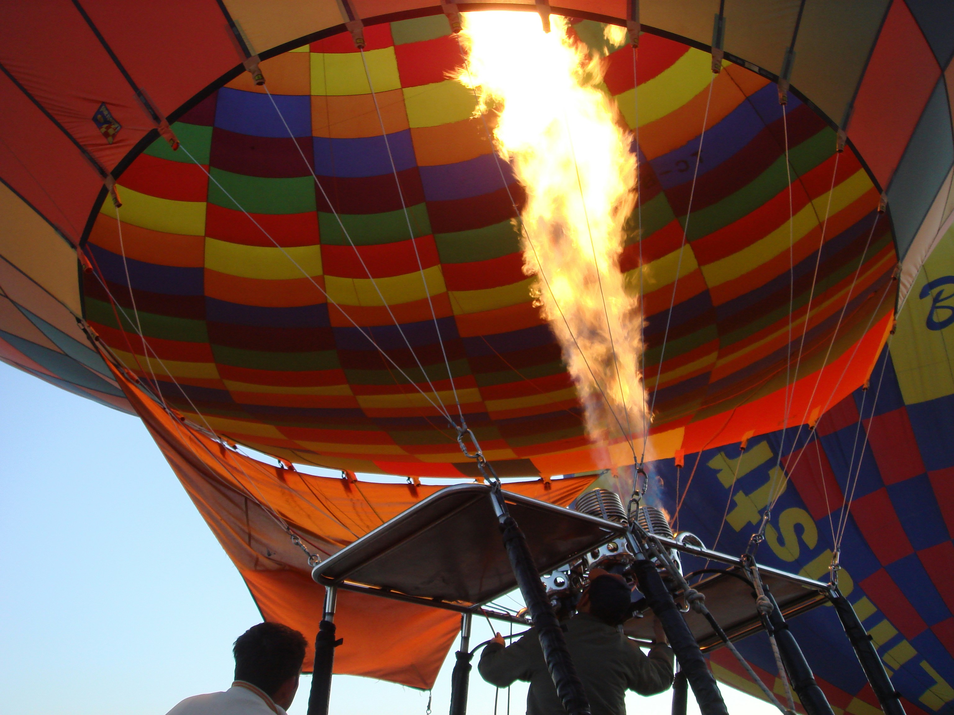Vibrant hot air balloon from below, showcasing the colorful canopy and the flame igniting the burner. The scene captures the essence of adventure and flight.