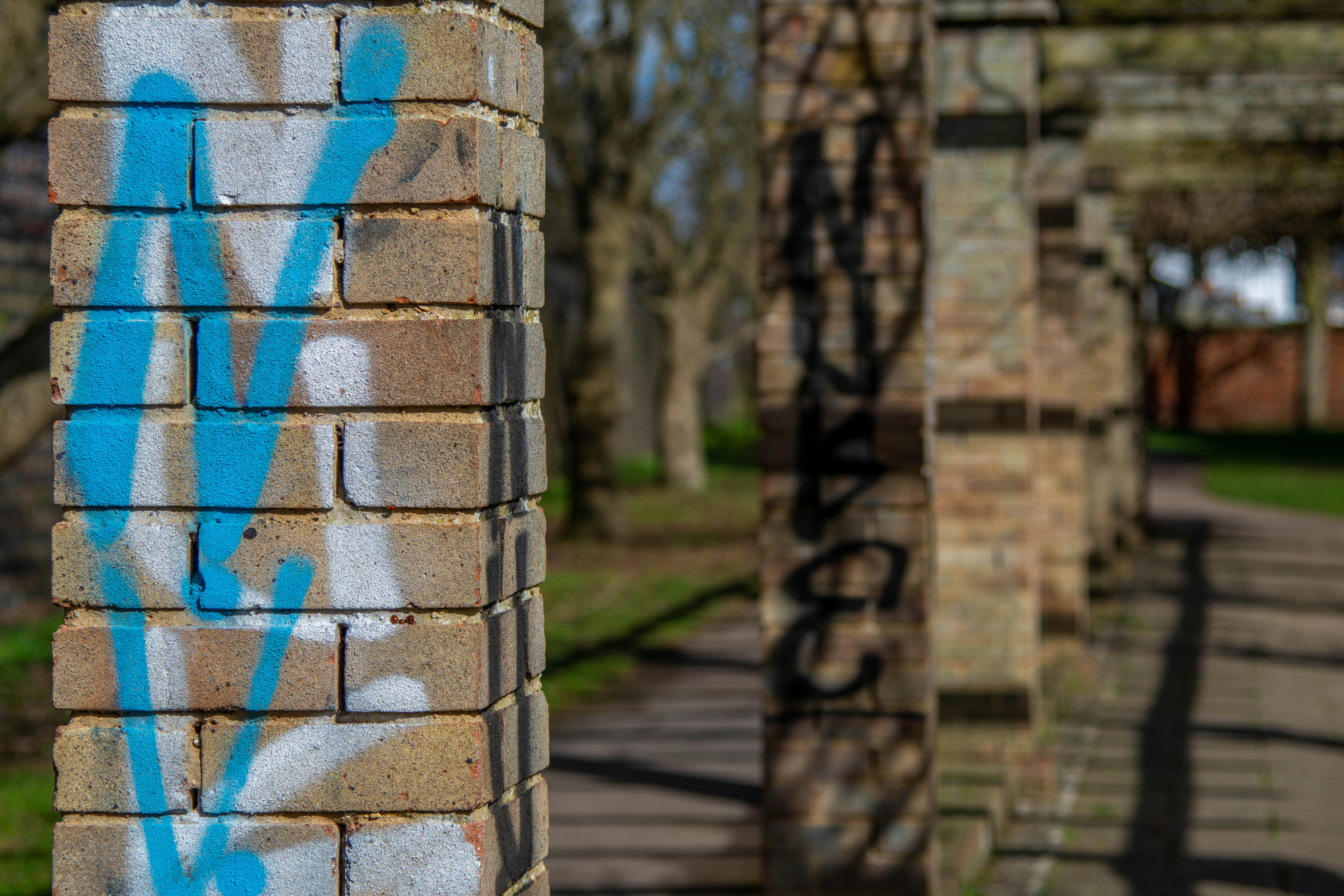 Blue Graffiti on a Brick Pillar Framing a Quiet Campus Walkway