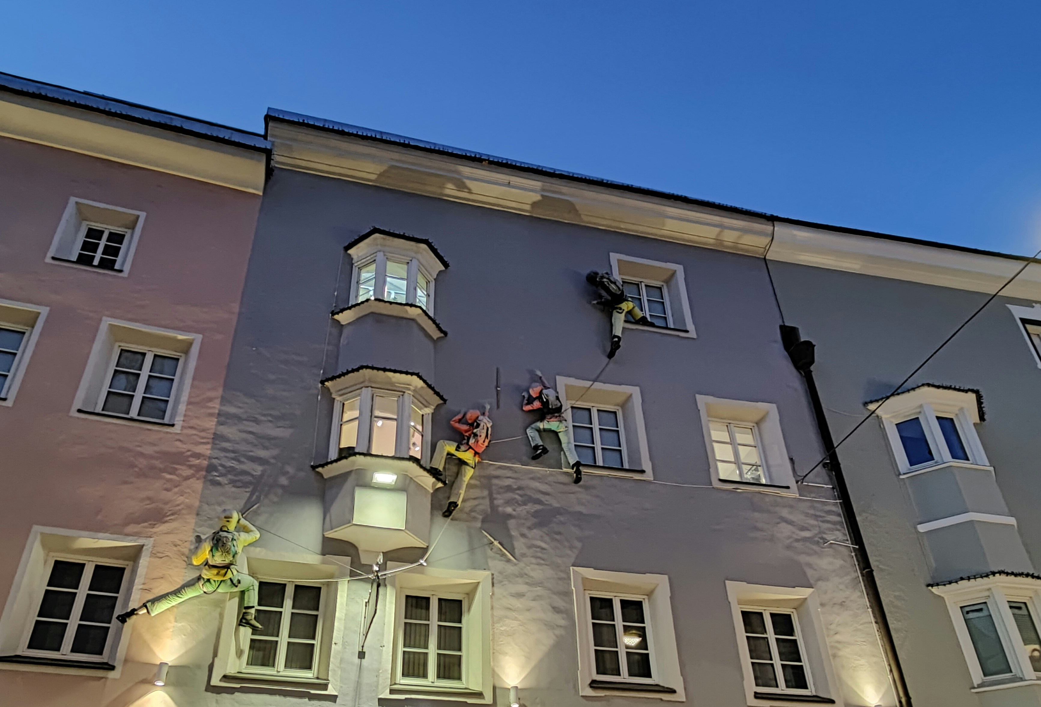 Dusk scene of a building facade adorned with playful human sculptures scaling the walls.