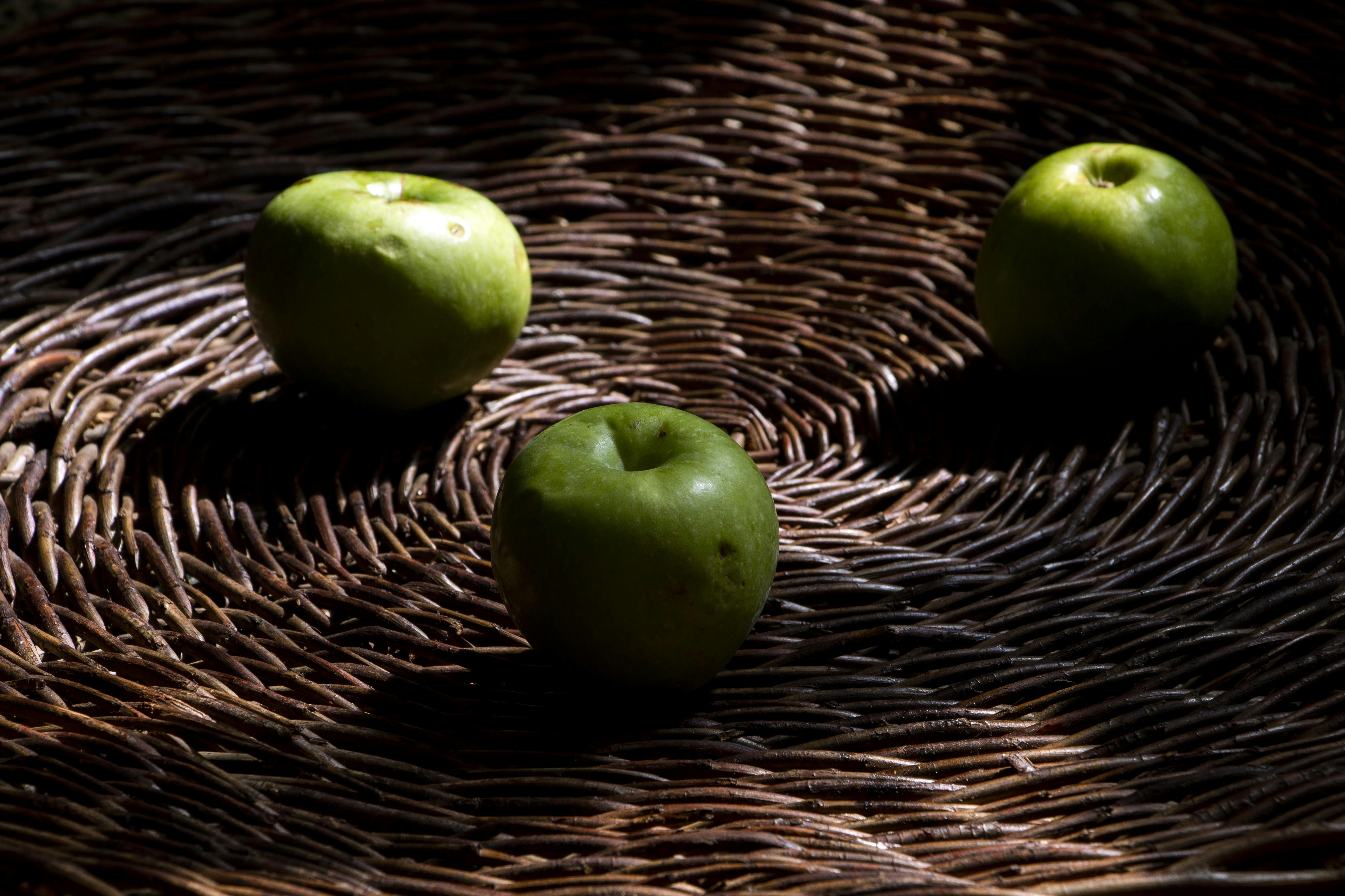 three green apples sitting in a wicker basket