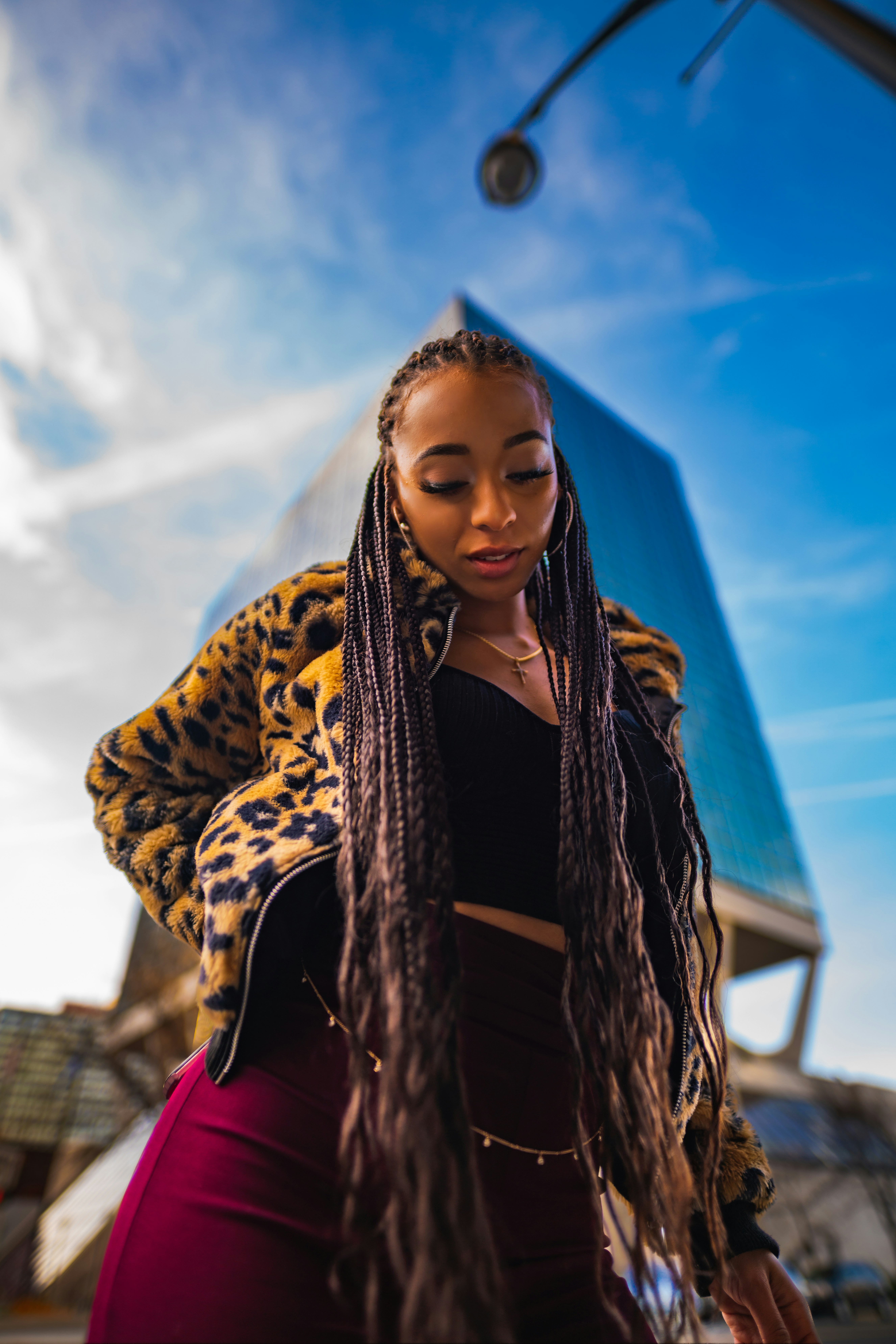 Person in a leopard print jacket poses confidently in front of a modern architectural structure under a blue sky.