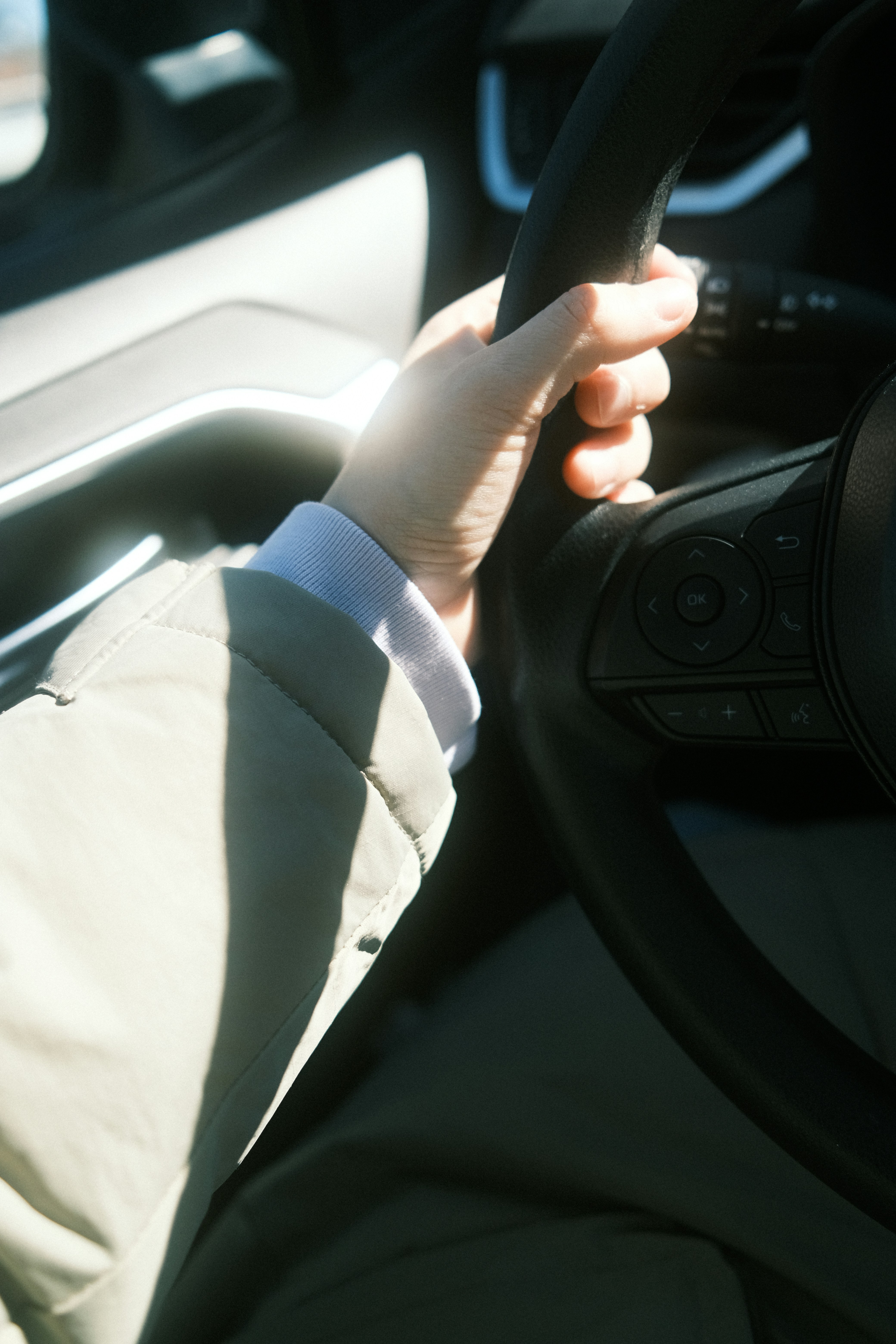 A hand grasping a car steering wheel, showcasing the intimate connection between driver and vehicle. The interior setting highlights modern automotive design.
