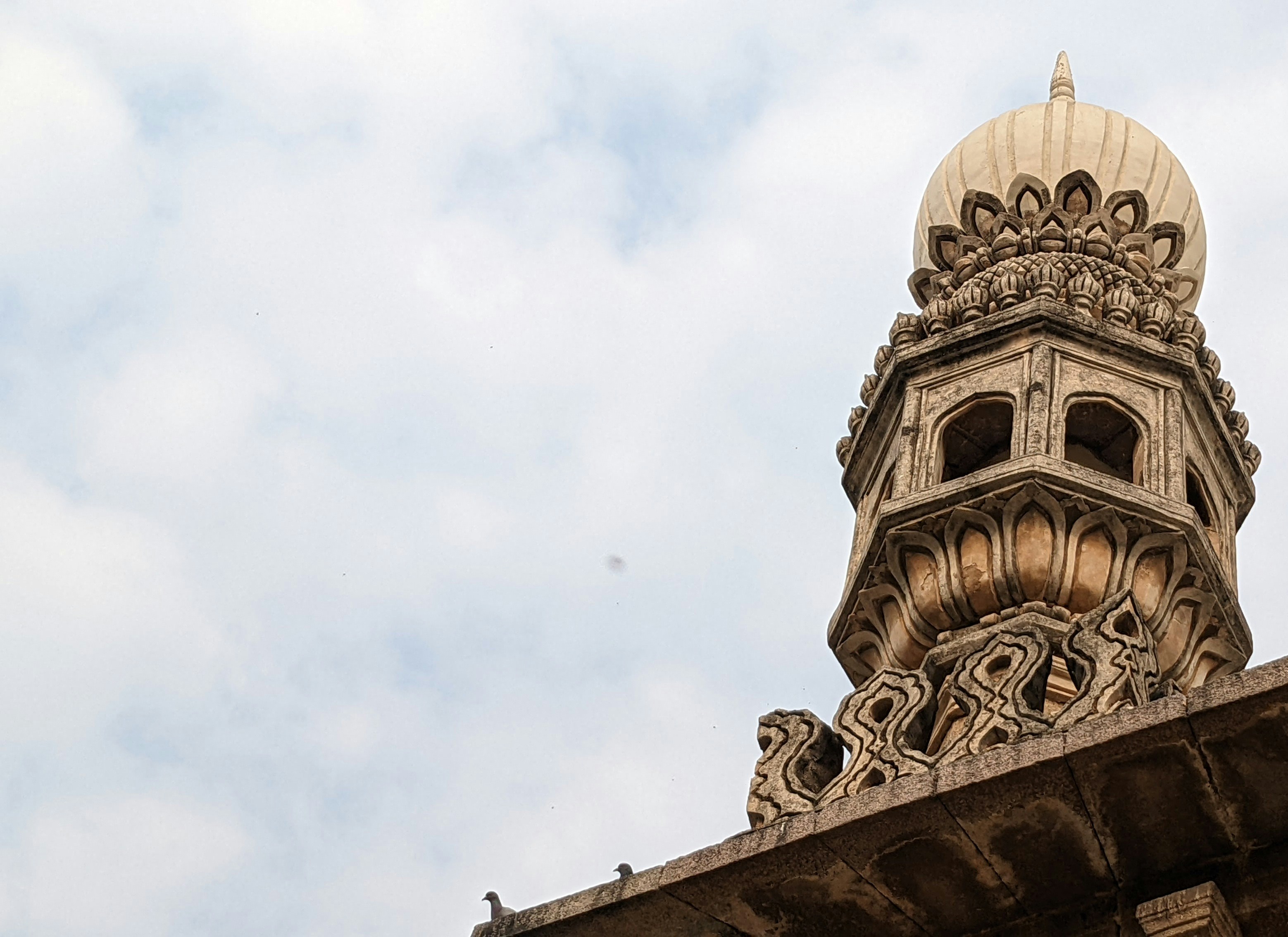 Elaborate architectural tower featuring intricate carvings and a domed top against a cloudy sky.