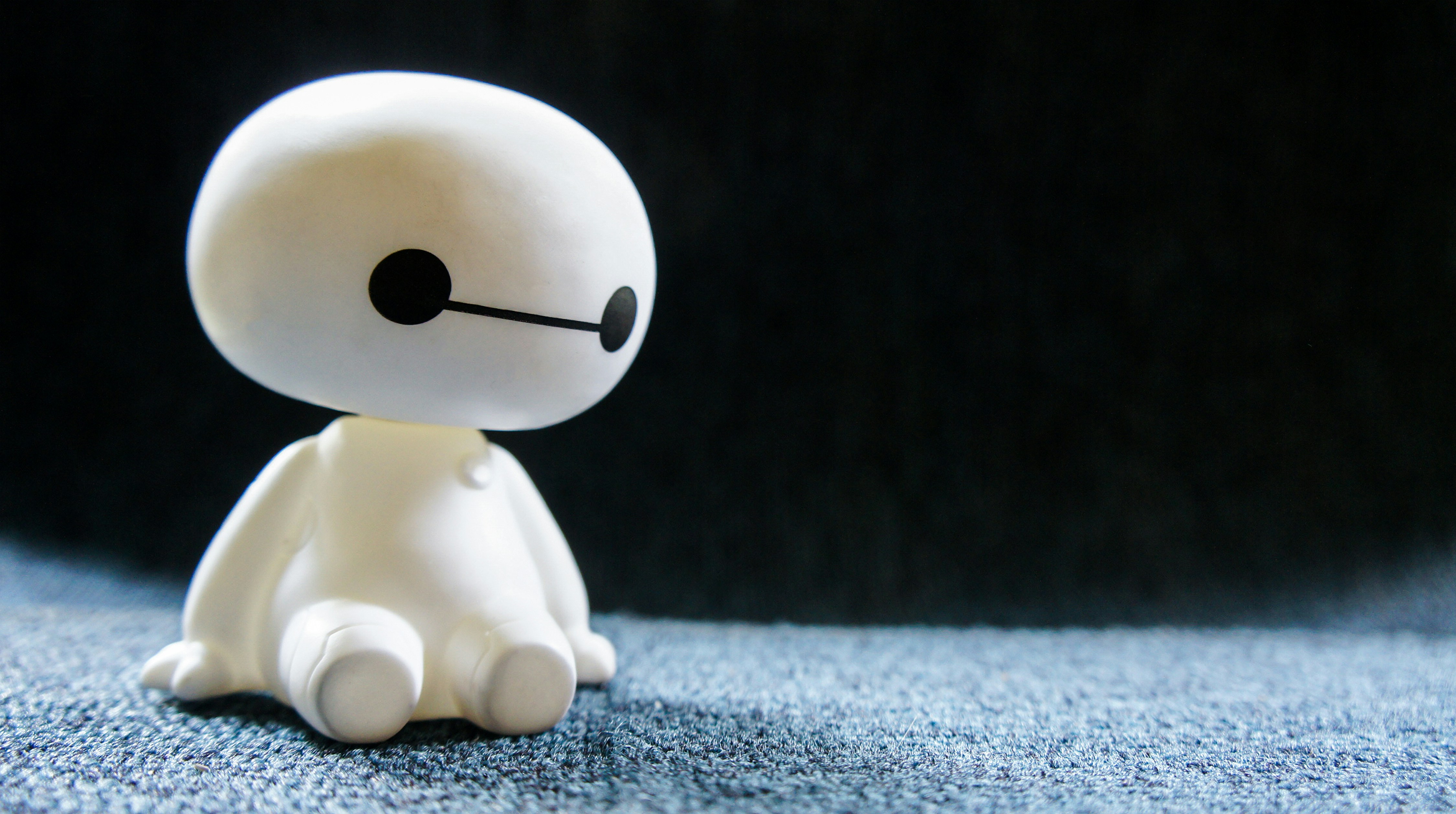 A charming white figurine with a simplistic design sits on a textured blue surface, evoking a sense of playfulness and innocence.