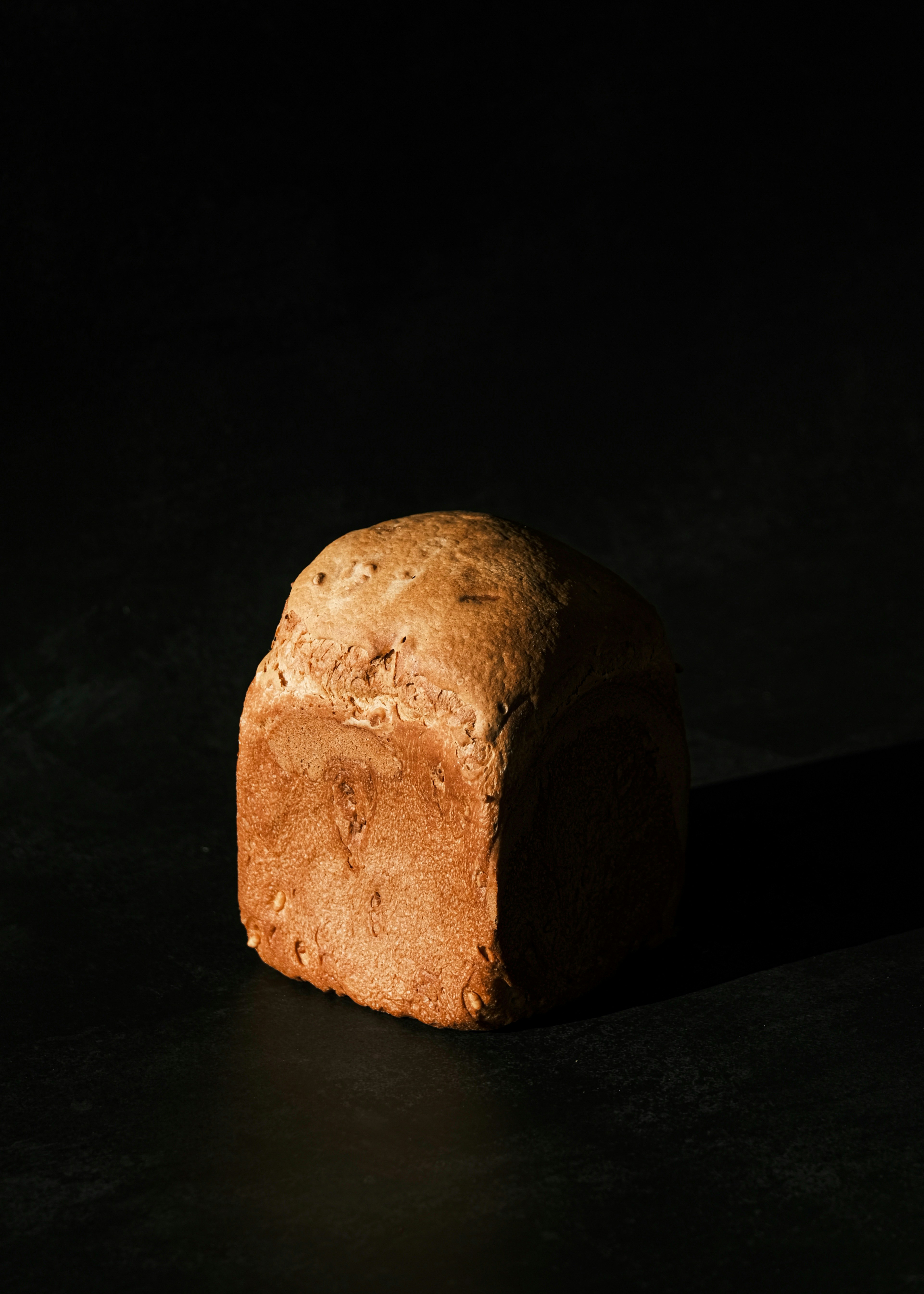 Freshly baked loaf of bread illuminated by soft light against a dark backdrop, showcasing its crusty texture and shape.