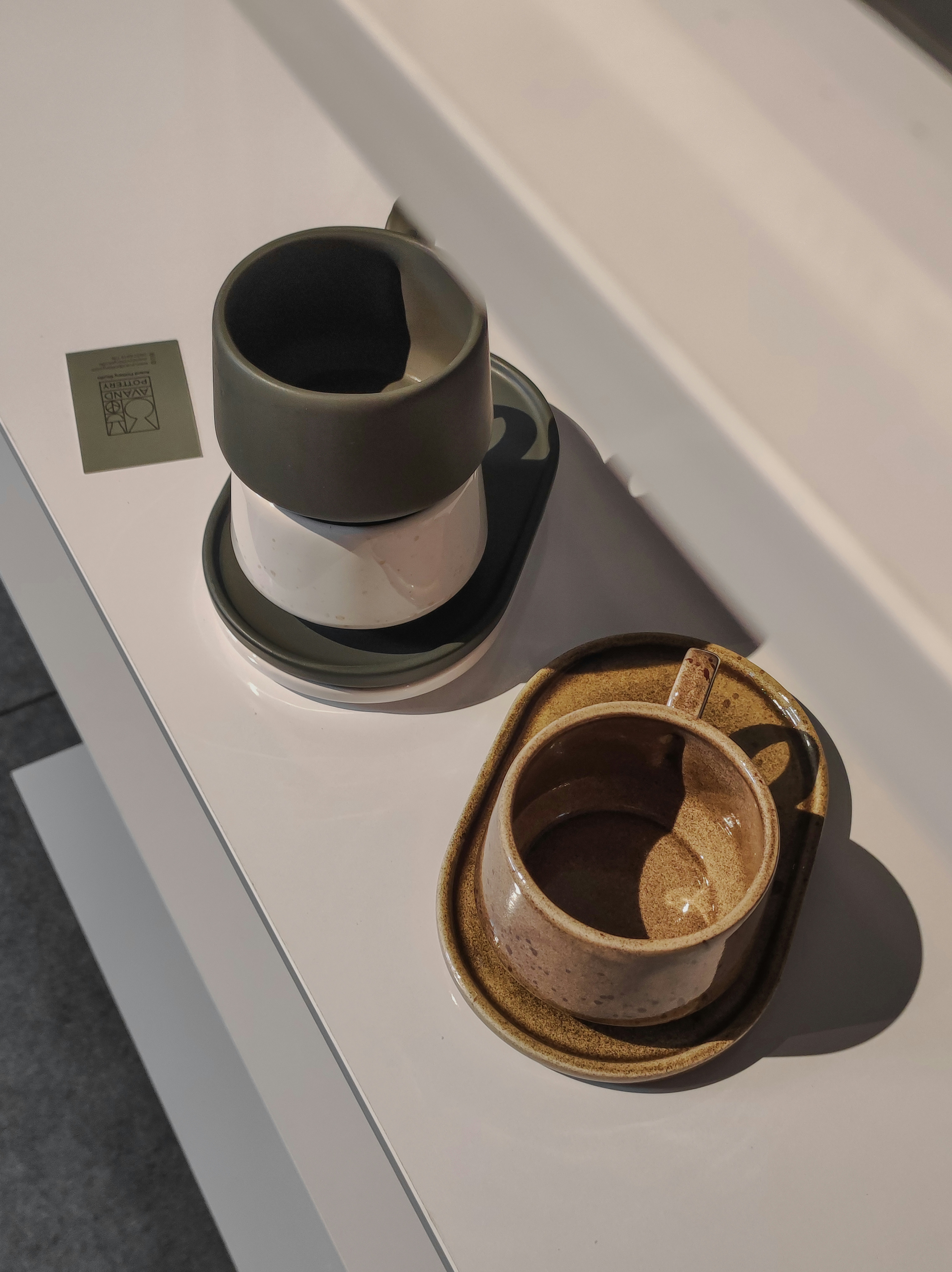 Two ceramic mugs on a white surface with subtle shadows and a small label nearby; a study in minimal still-life lighting.