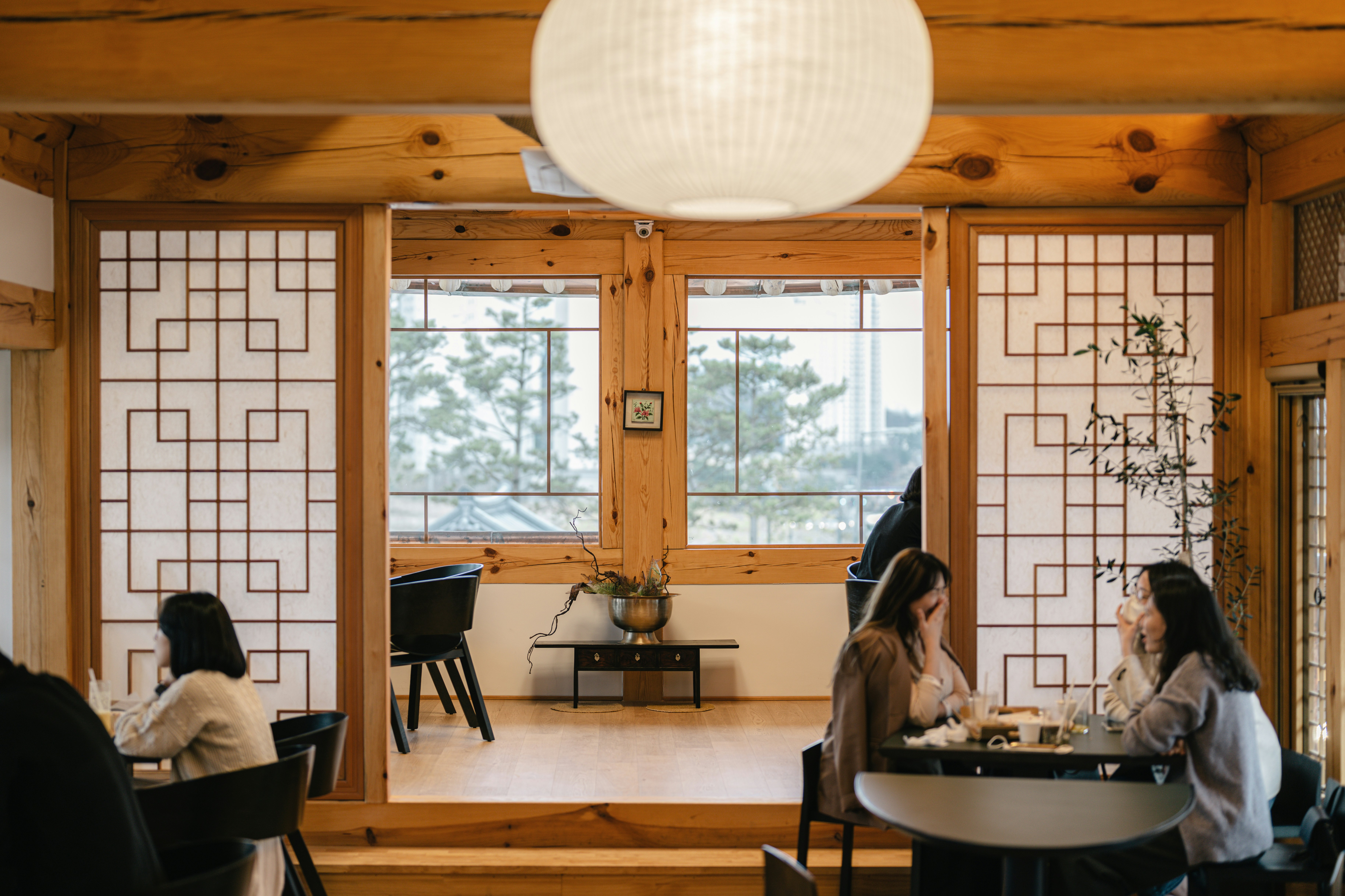 Cozy tea room featuring wooden architecture and patrons enjoying their time. Natural light filters through decorative screens, enhancing the serene atmosphere.