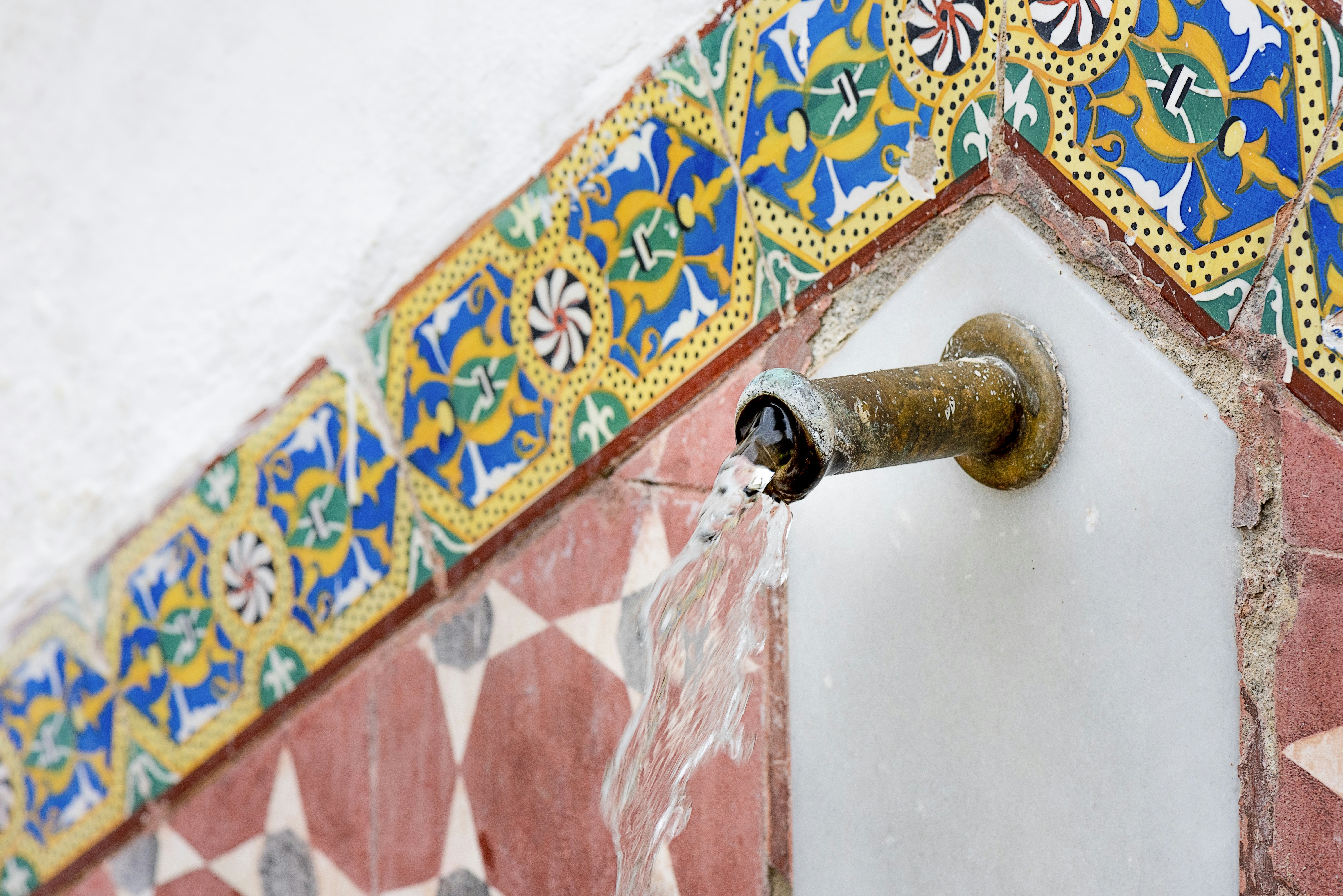 Water Trickles from a Turquoise-Tiled Spout: A Quiet Moment in a Colorful Tile Border