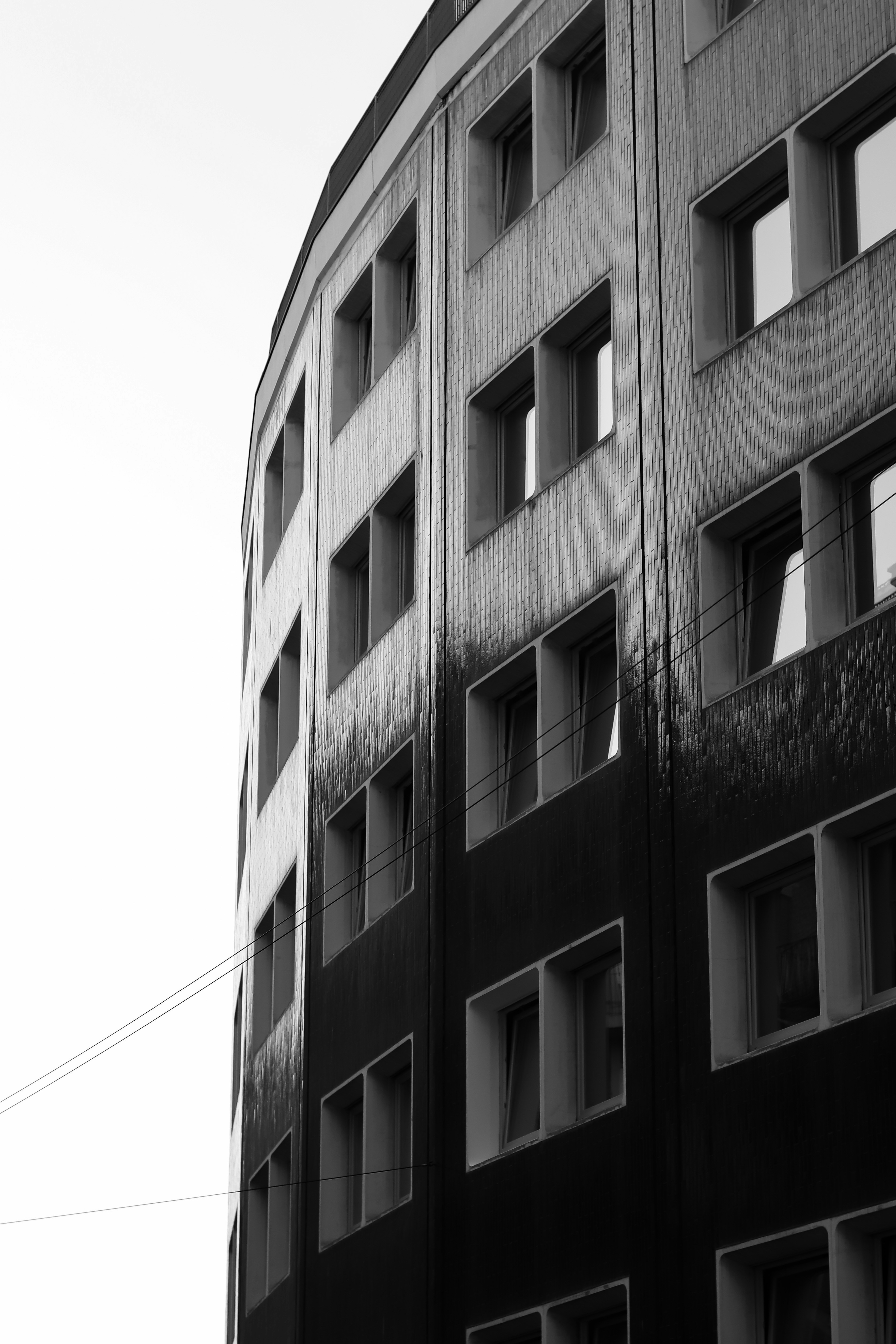 A close-up view of a modern building's façade, showcasing the interplay of light and shadow on its textured surfaces in black and white.