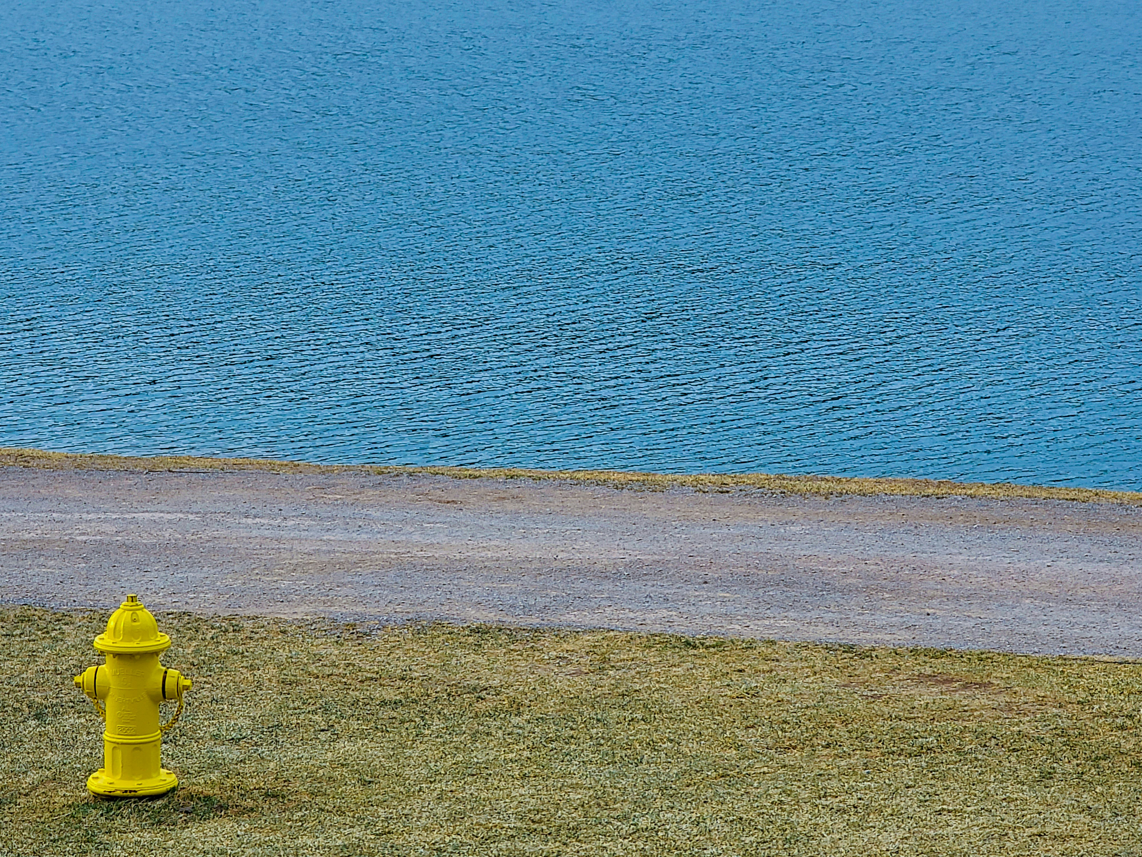Bright yellow fire hydrant stands on grassy shore beside tranquil blue water, creating a striking visual contrast.