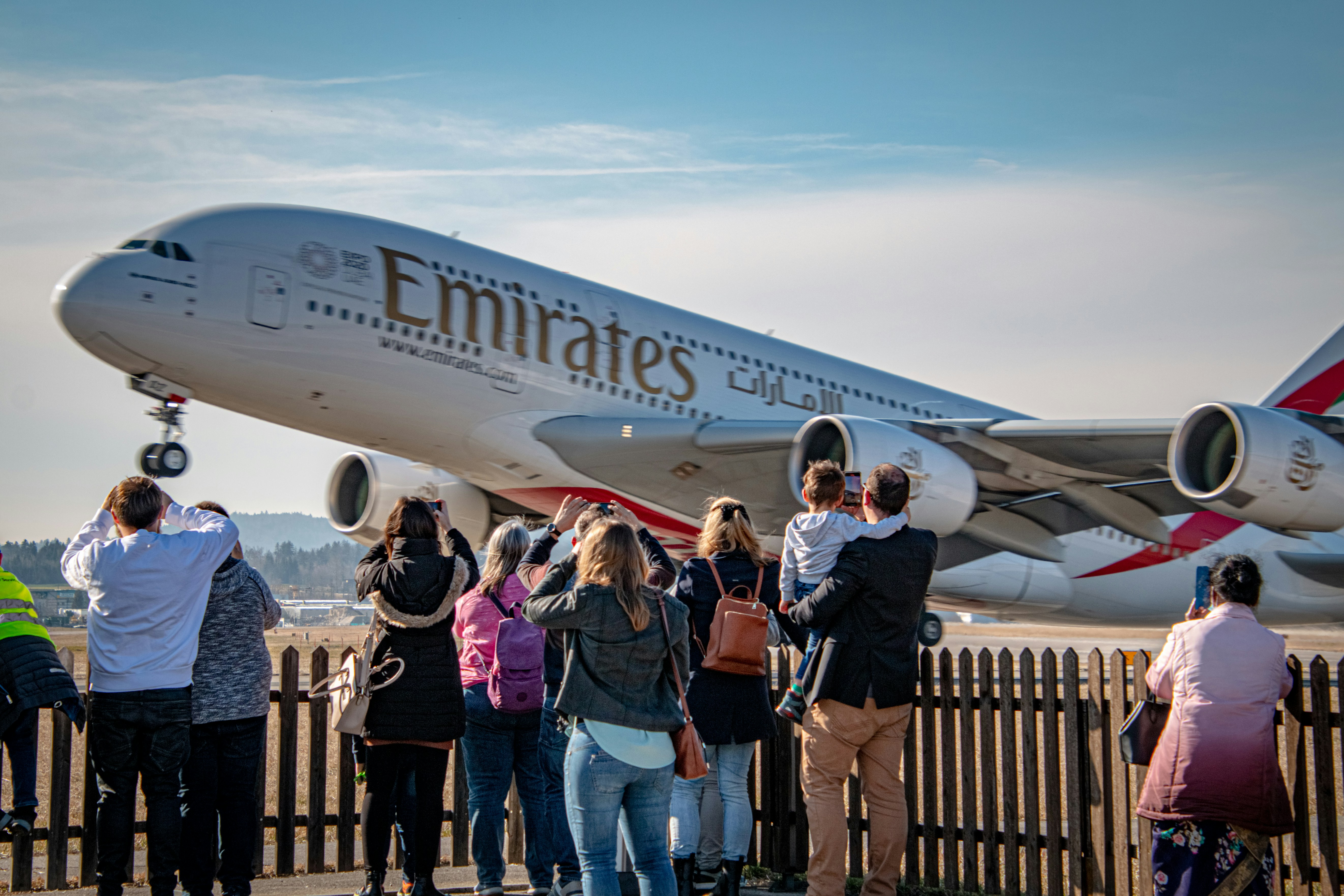 Emirates A380 on Display: Curious Onlookers Gather Along a Fence Under a Clear Blue Sky
