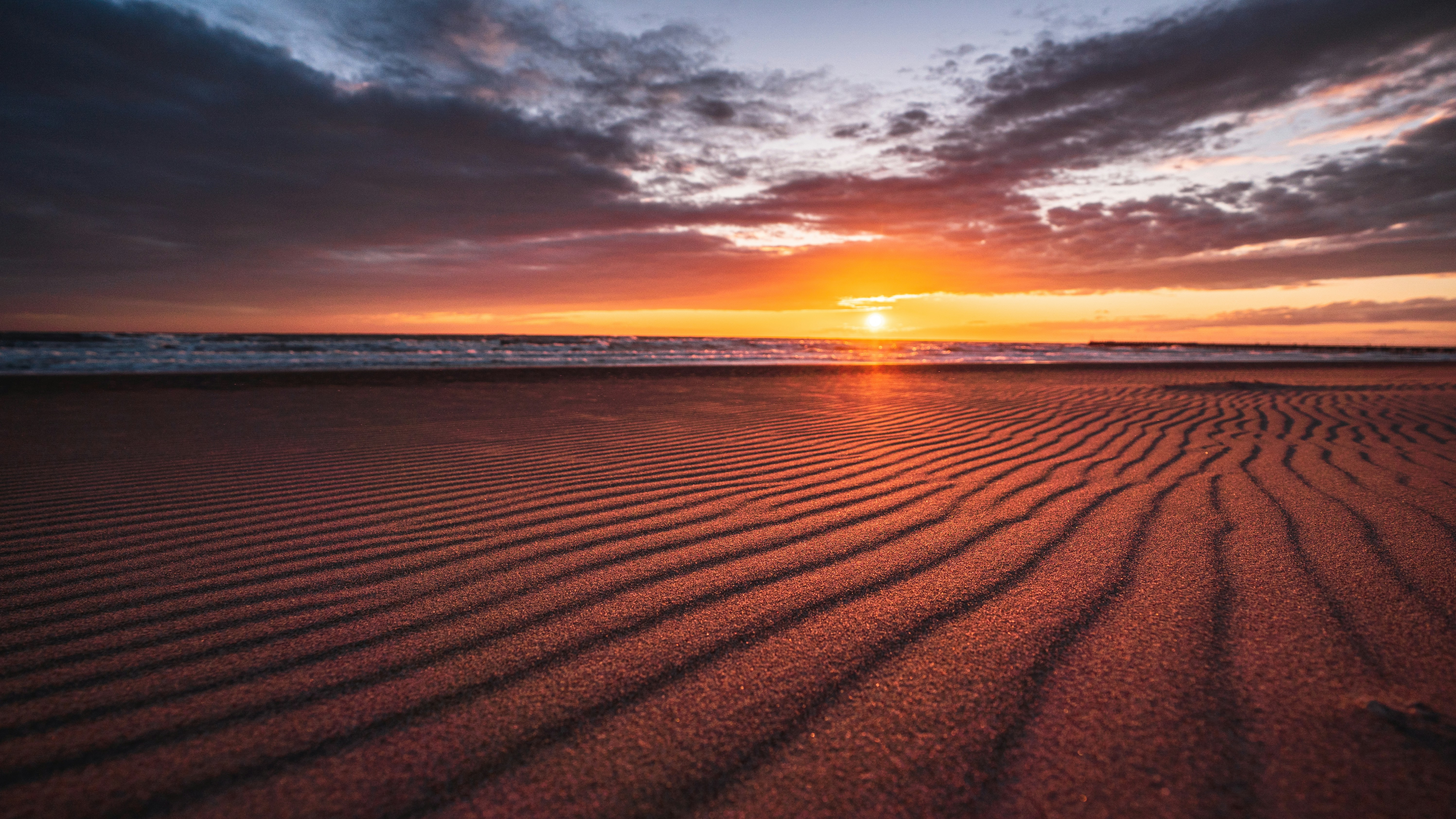 Sunset over a beach with rippled sand patterns leading to the horizon.