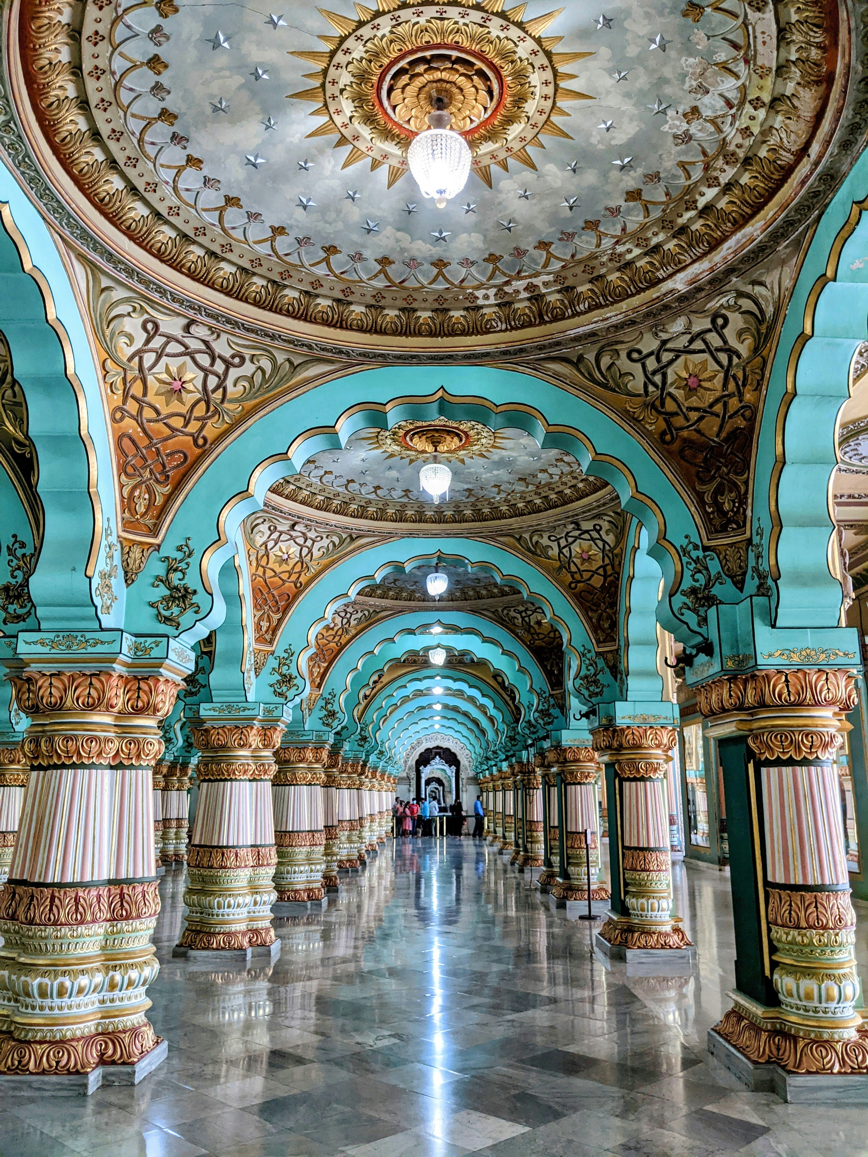 Intricate turquoise arches and ornate columns create a stunning corridor in a historic palace. Soft lighting enhances the detailed craftsmanship throughout the space.