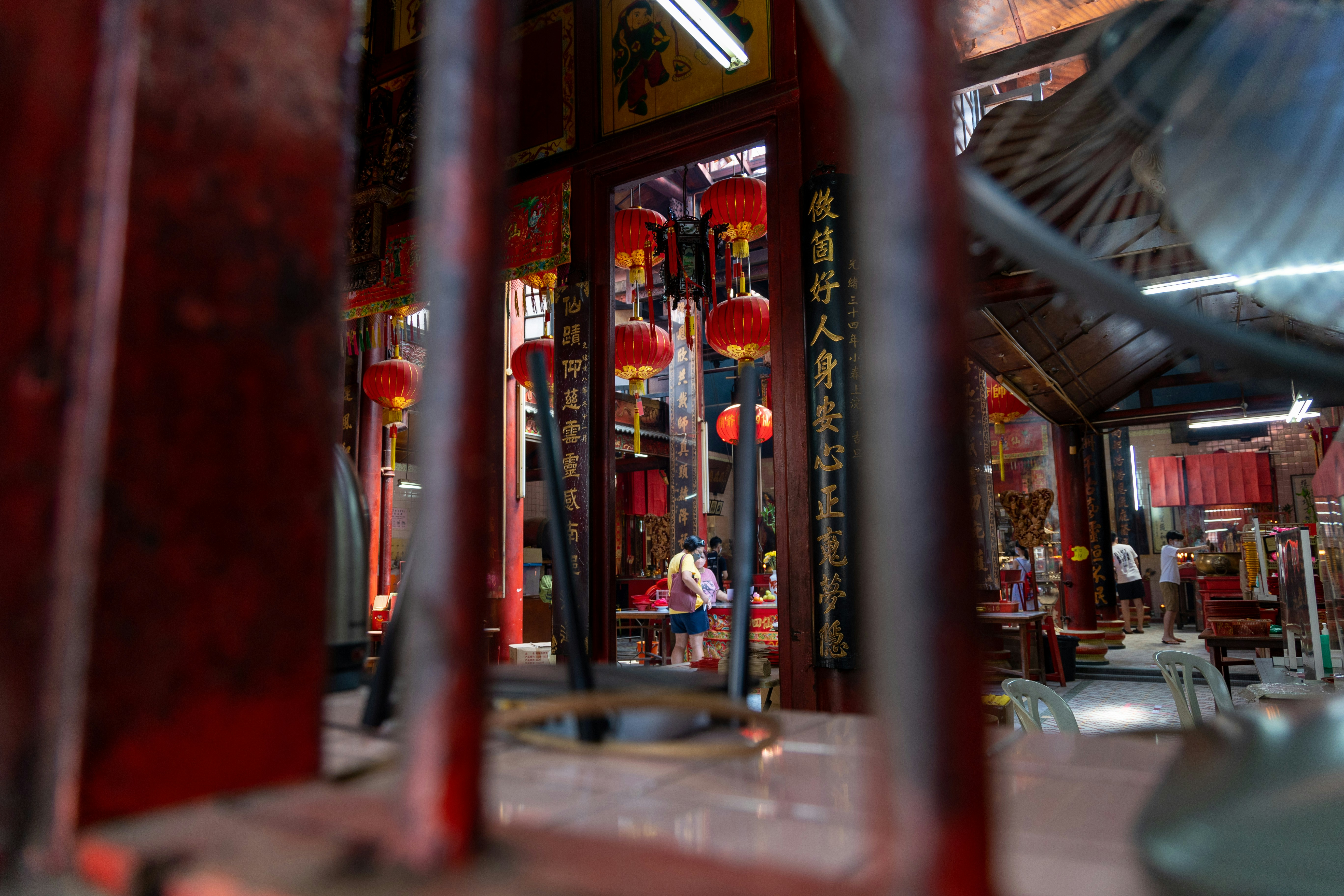 Intricate lanterns and vibrant decor inside a traditional temple framed through red iron bars.
