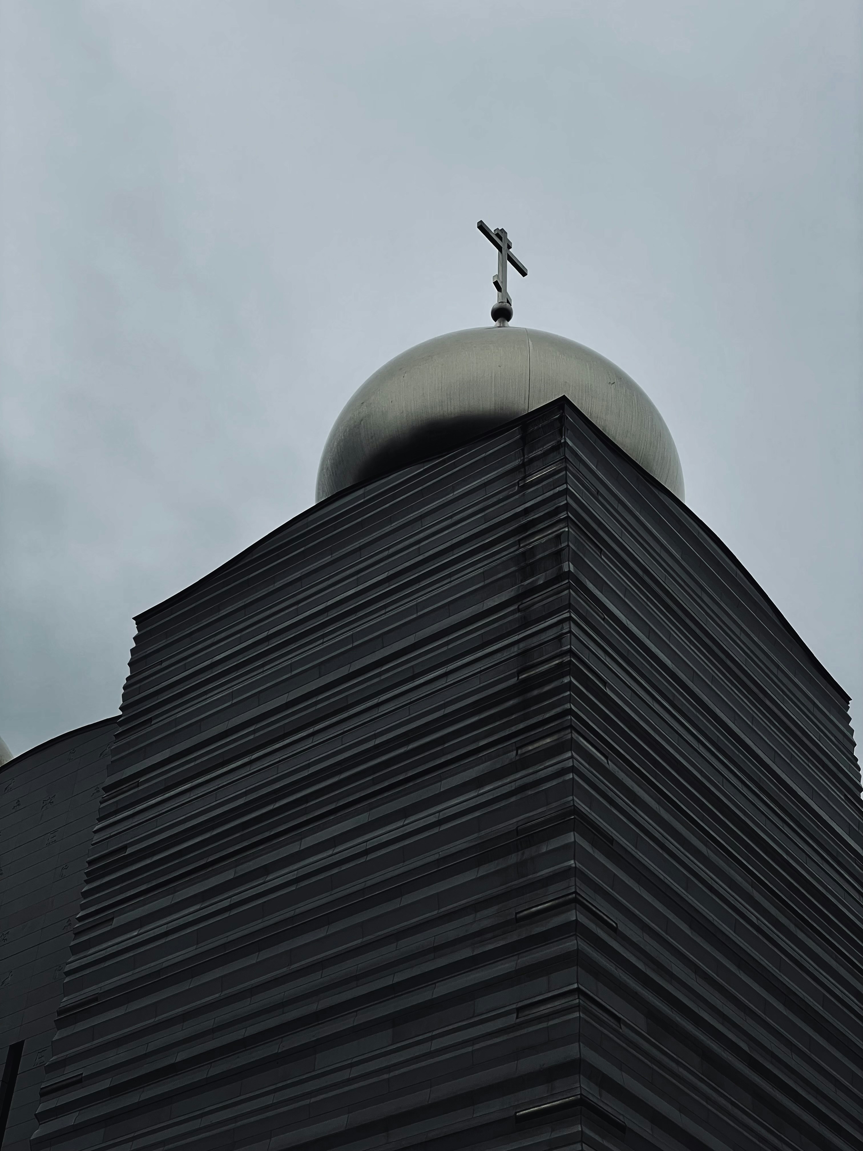 Sleek black building with a prominent silver dome topped by a cross against a cloudy sky.