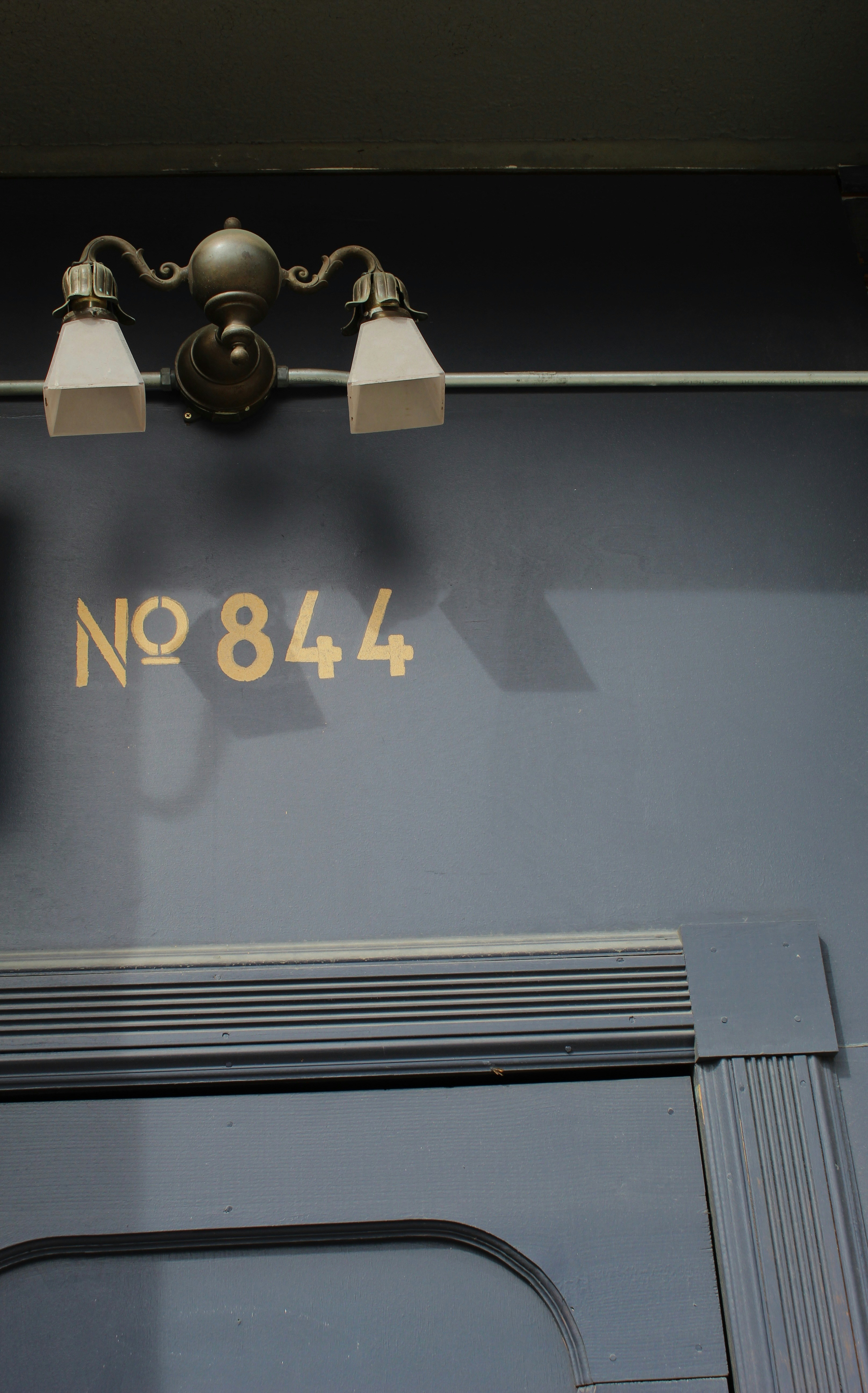 Vintage wall-mounted lights illuminate the number 844, set against a deep blue backdrop, highlighting architectural details.