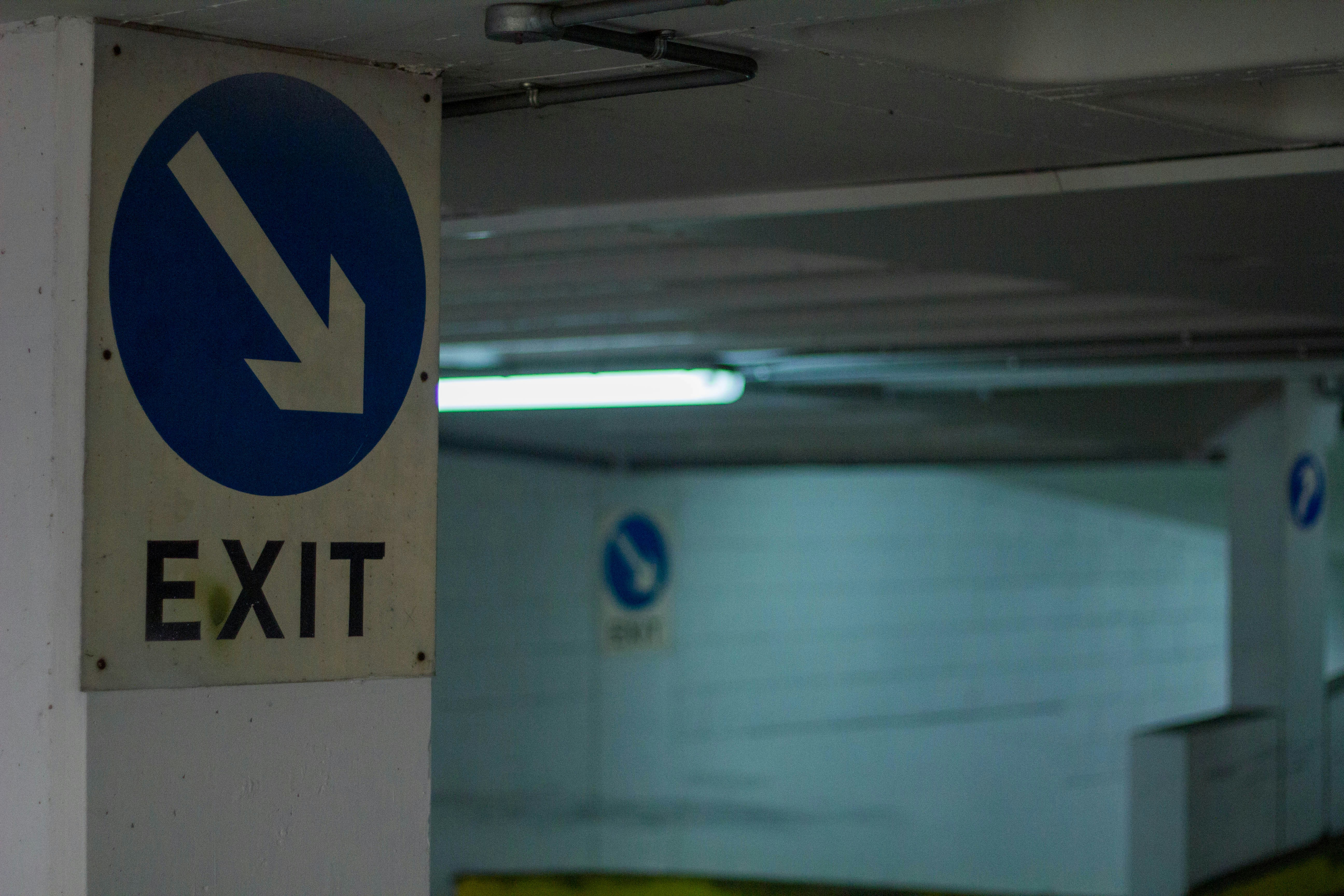 A blue exit sign hanging from the side of a white wall photo – Free ...