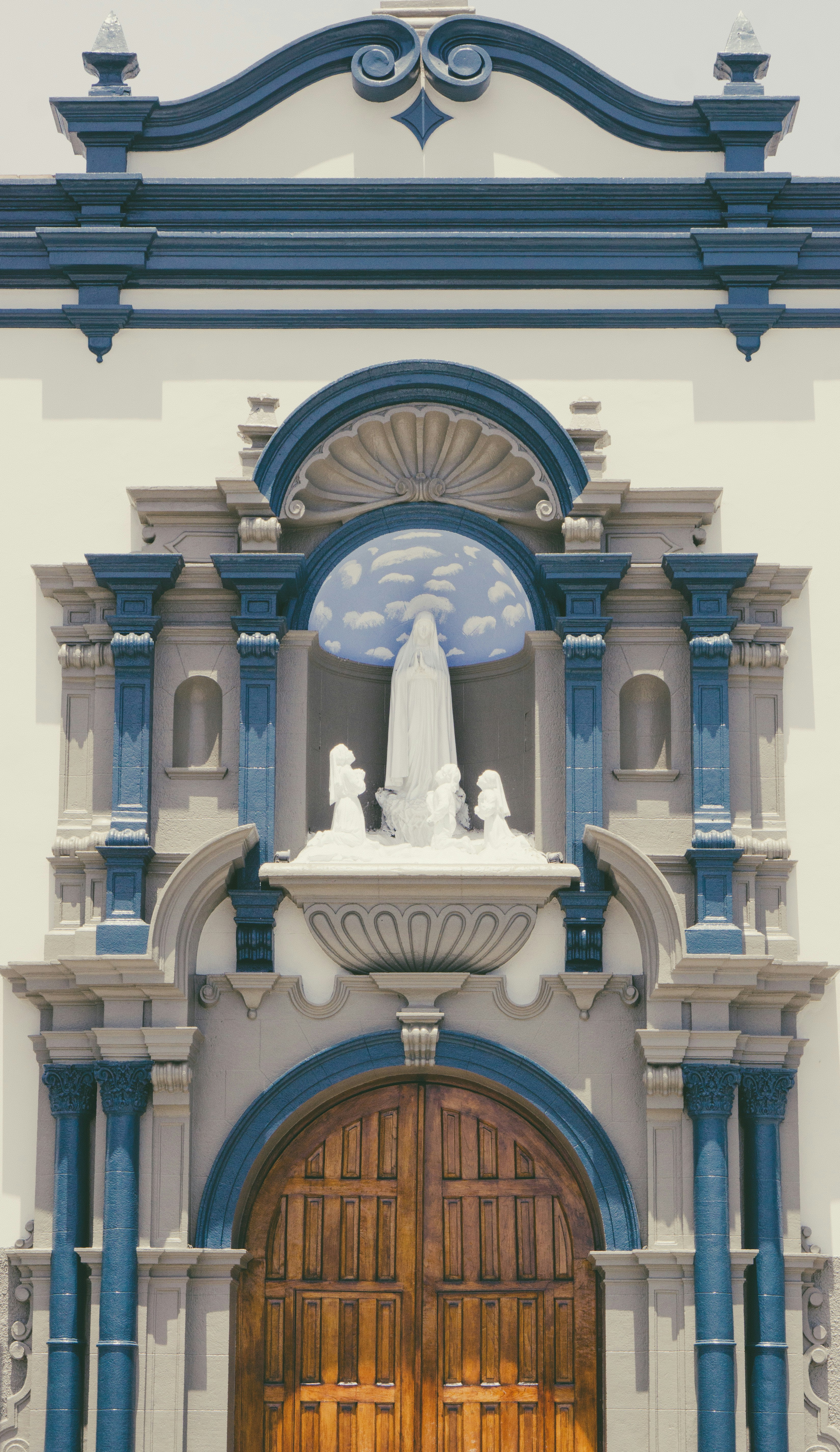 Intricate church facade featuring a statue of a religious figure surrounded by ornate architectural details and a wooden door.