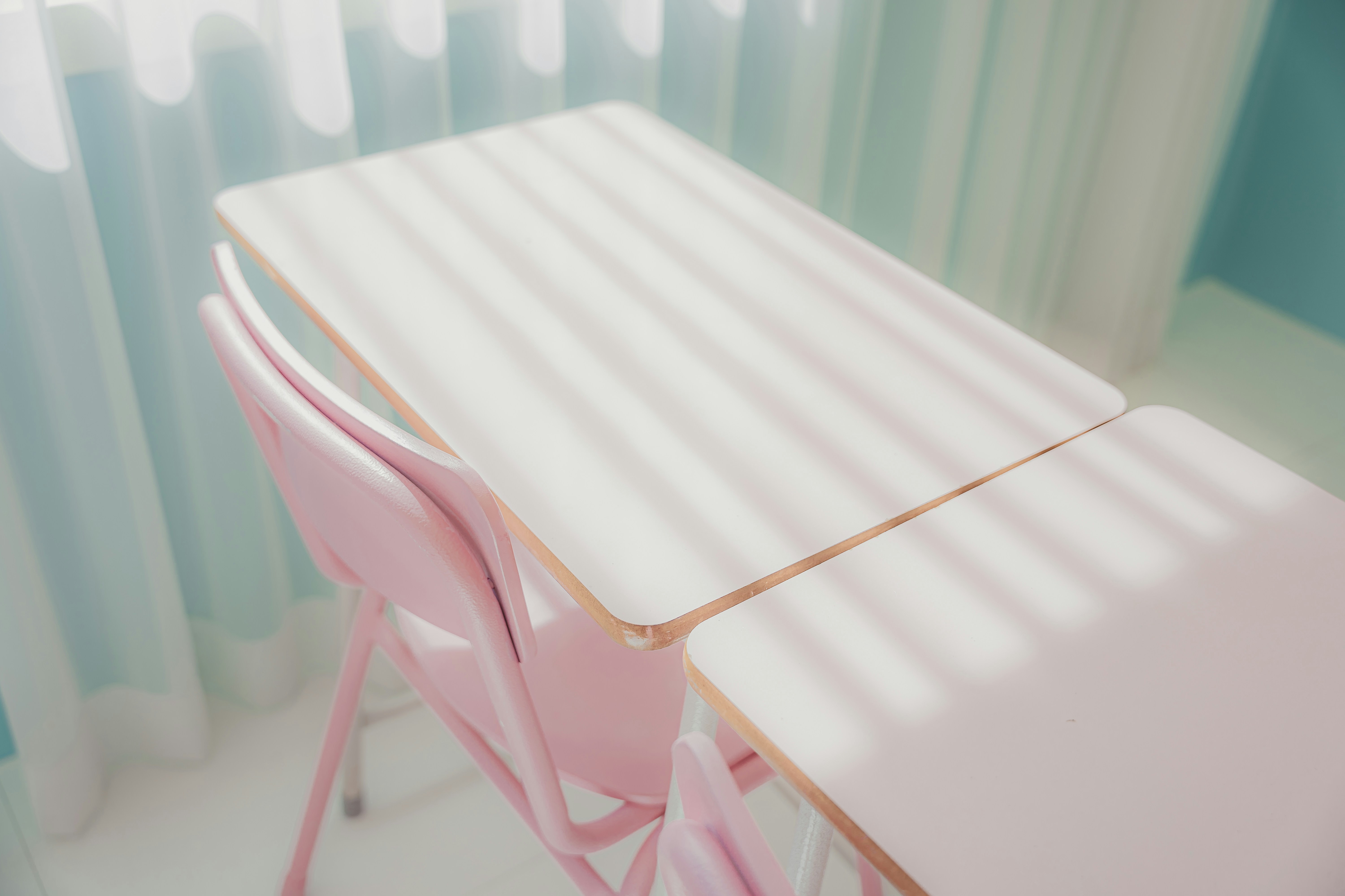 Soft pink chairs and white tabletops illuminated by gentle sunlight filtering through sheer curtains.