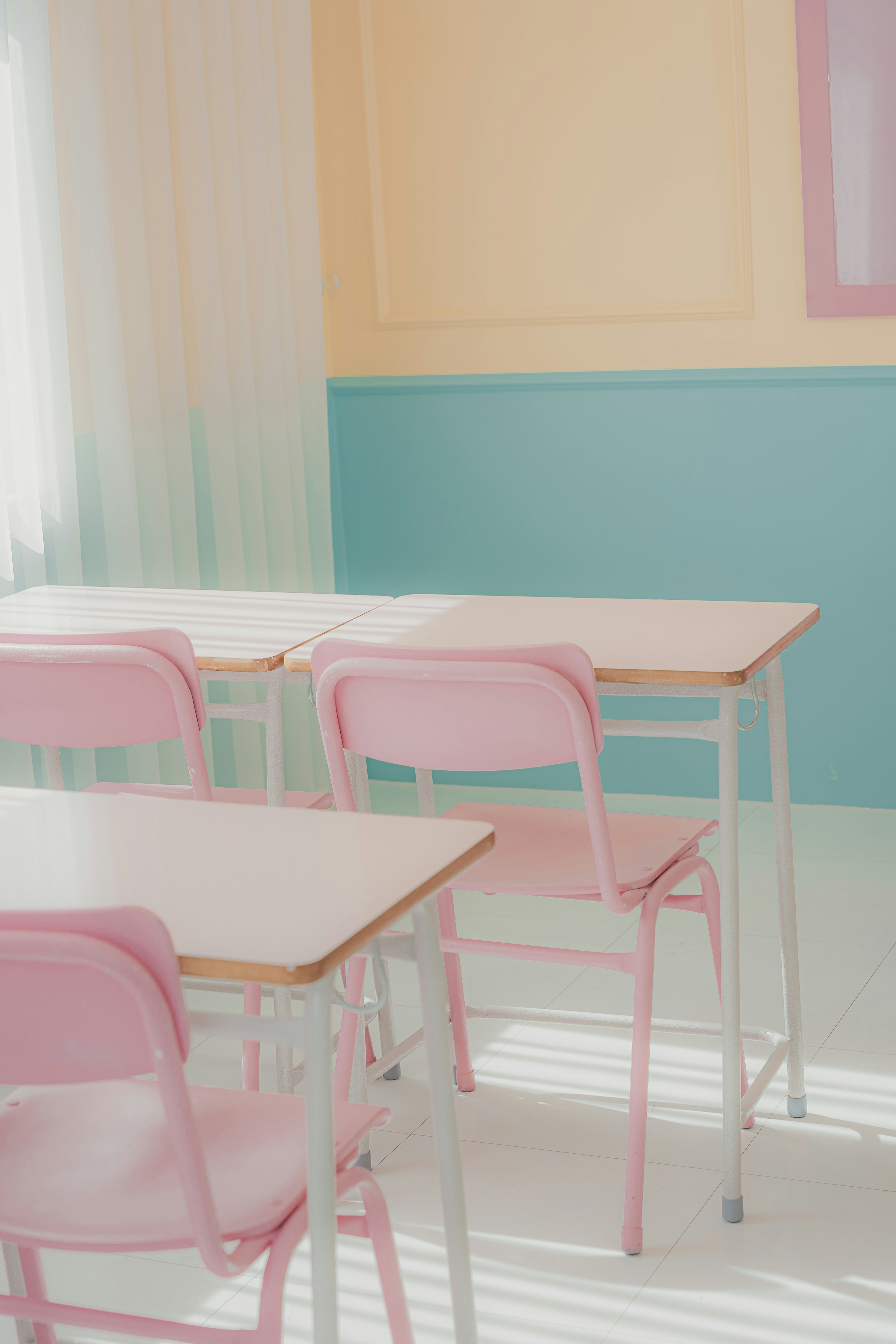 Bright classroom featuring pastel pink chairs and a soothing color palette of yellow and teal. Natural light filters through sheer curtains, enhancing the tranquil atmosphere.