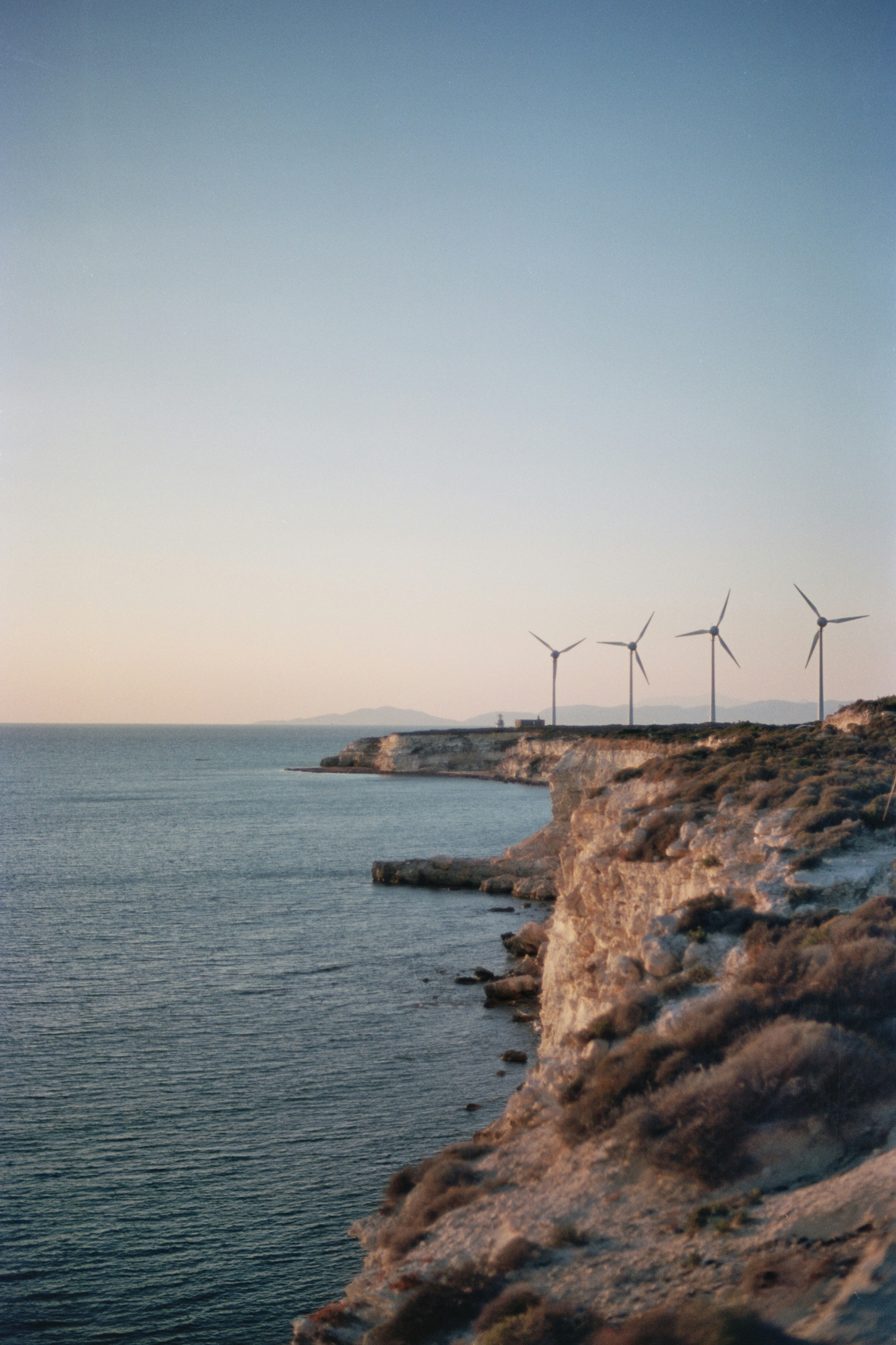 A row of wind turbines on a cliff near the ocean photo – Free Grey ...