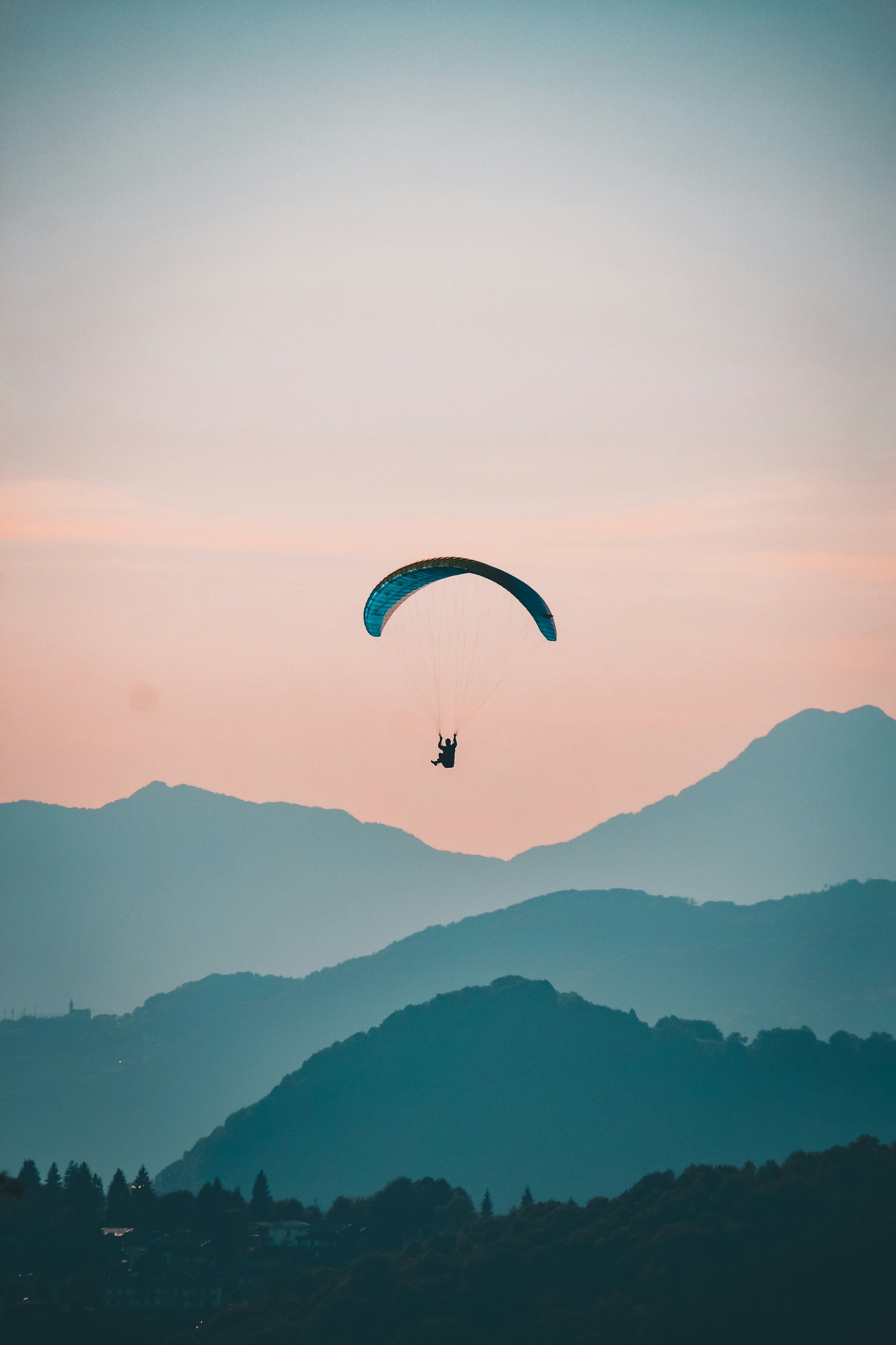 A paraglider gracefully descends against a backdrop of soft pastel skies and distant mountains, capturing the essence of adventure and freedom.