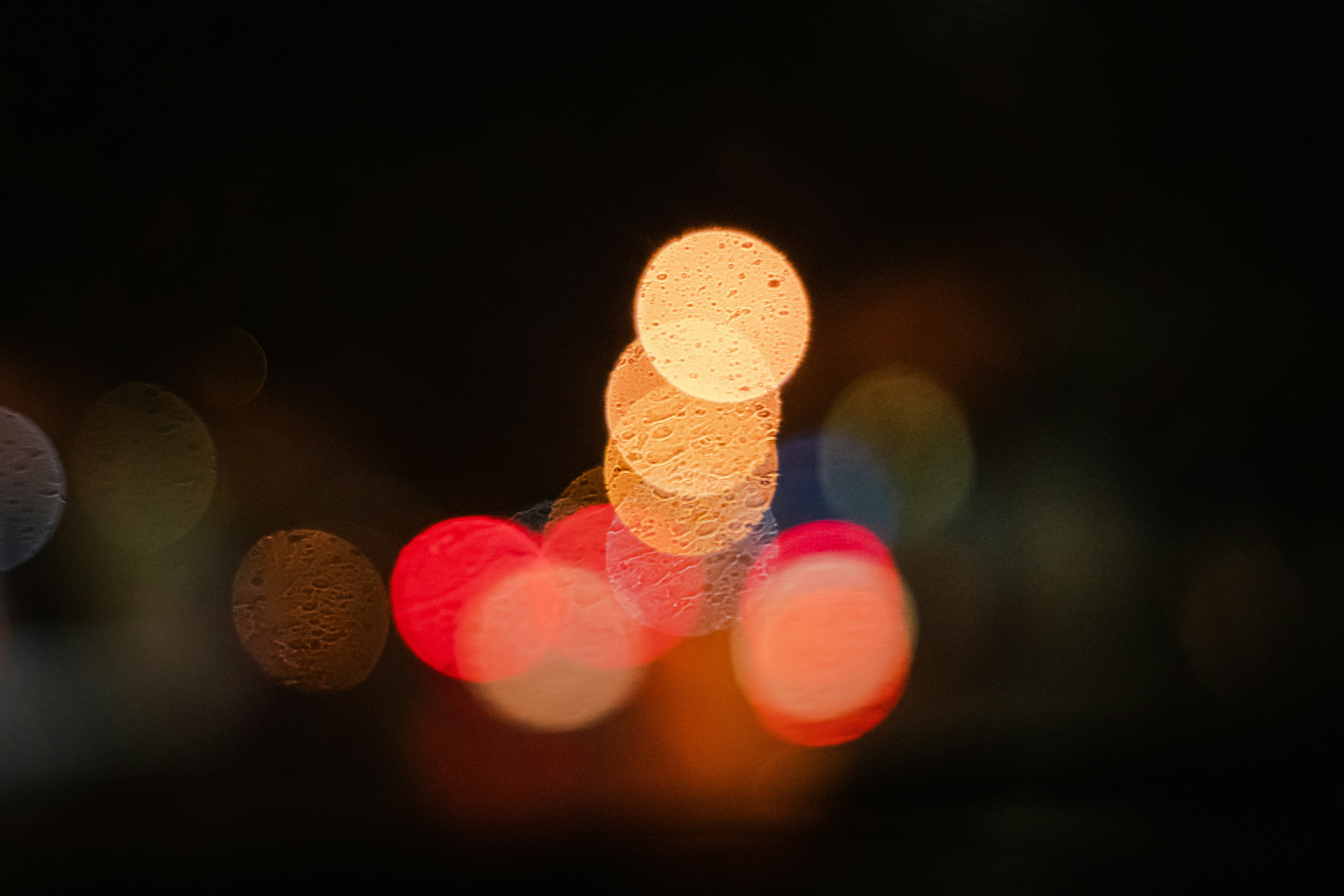 Colorful bokeh effects created by raindrops on a window, showcasing blurred city lights at night.
