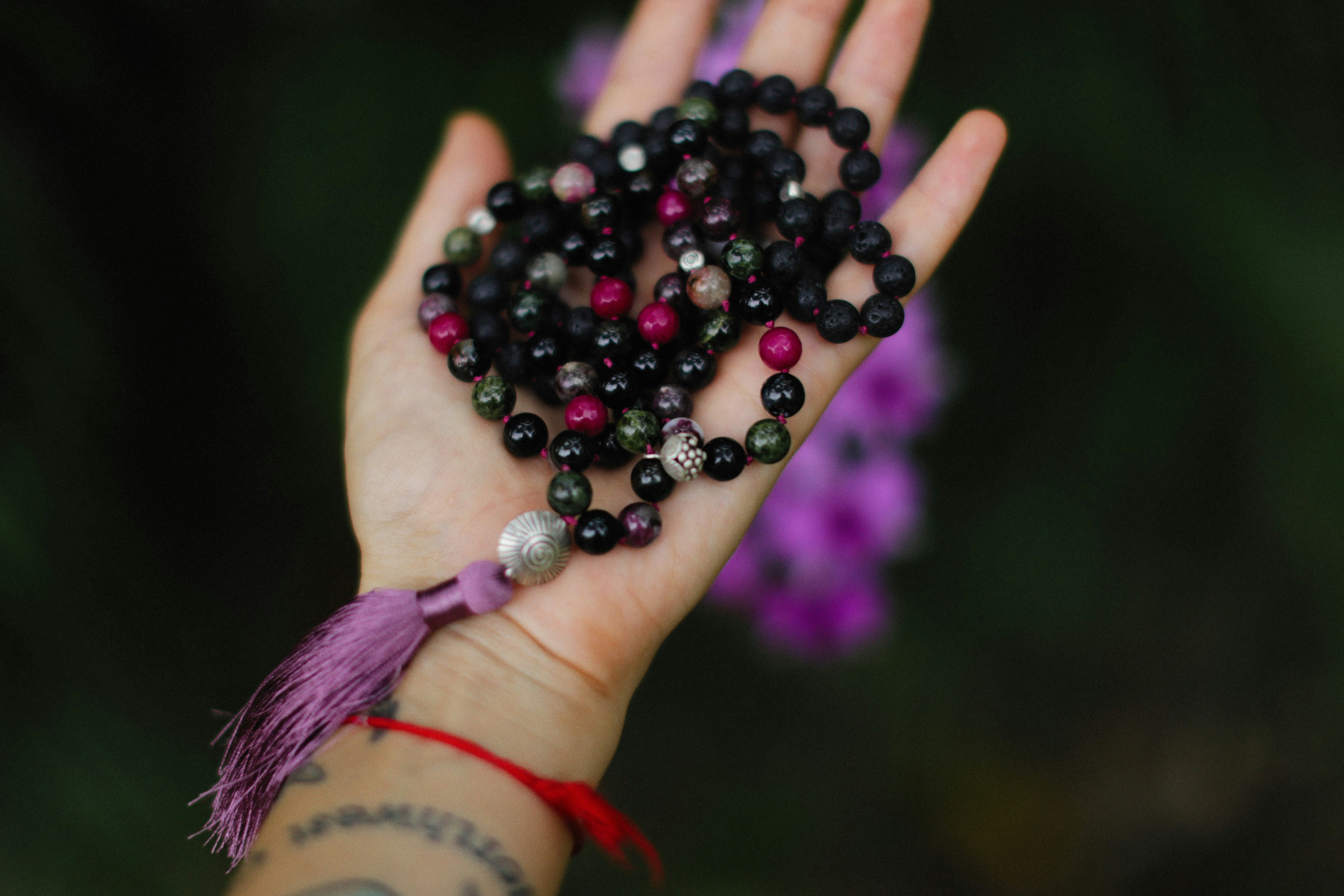 Beads in the Palm: a Quiet Moment of Colorful Prayer Strings Against a Blooming Backdrop