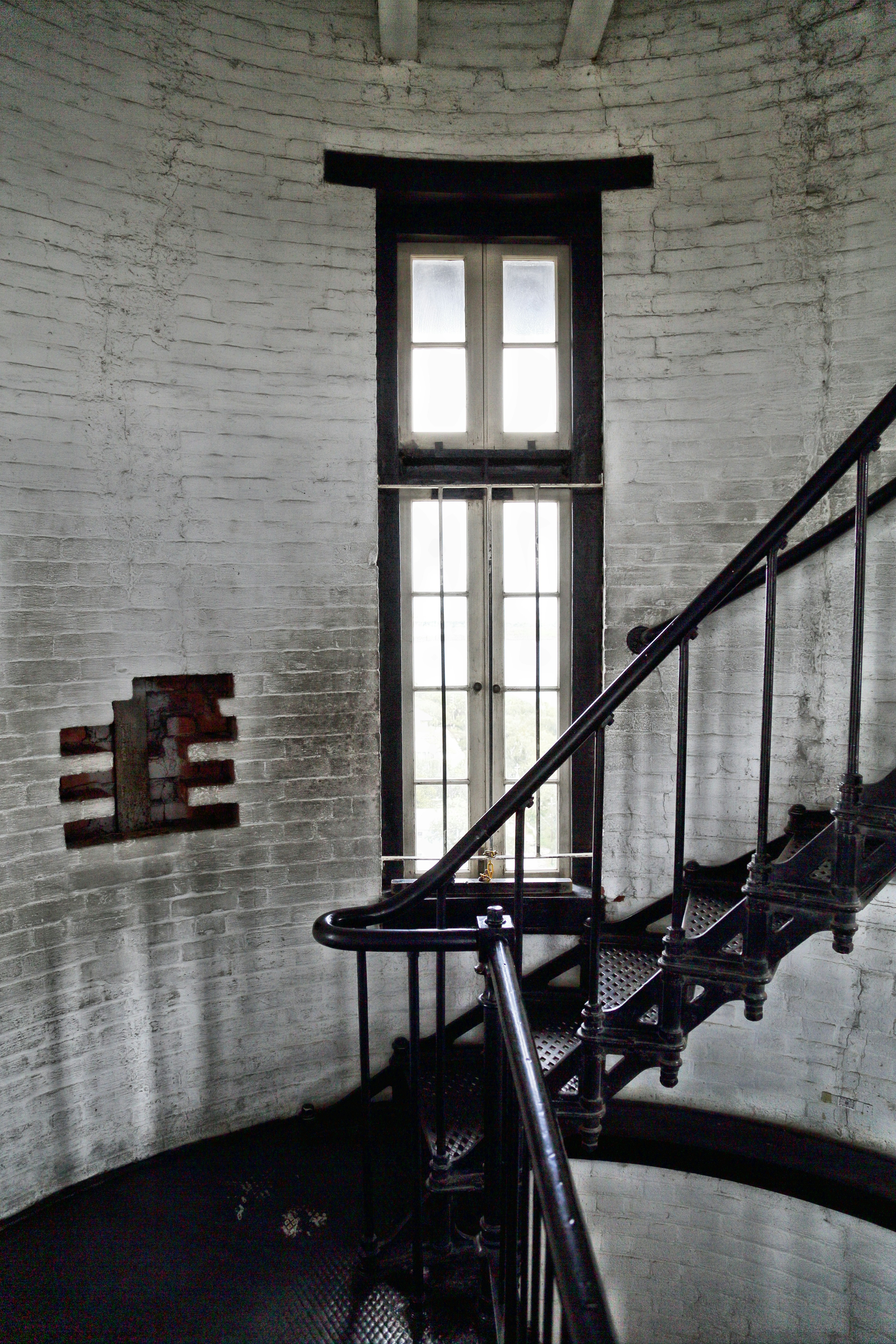 Iron Spiral Reaching Toward a Narrow Window in a White Brick Tower